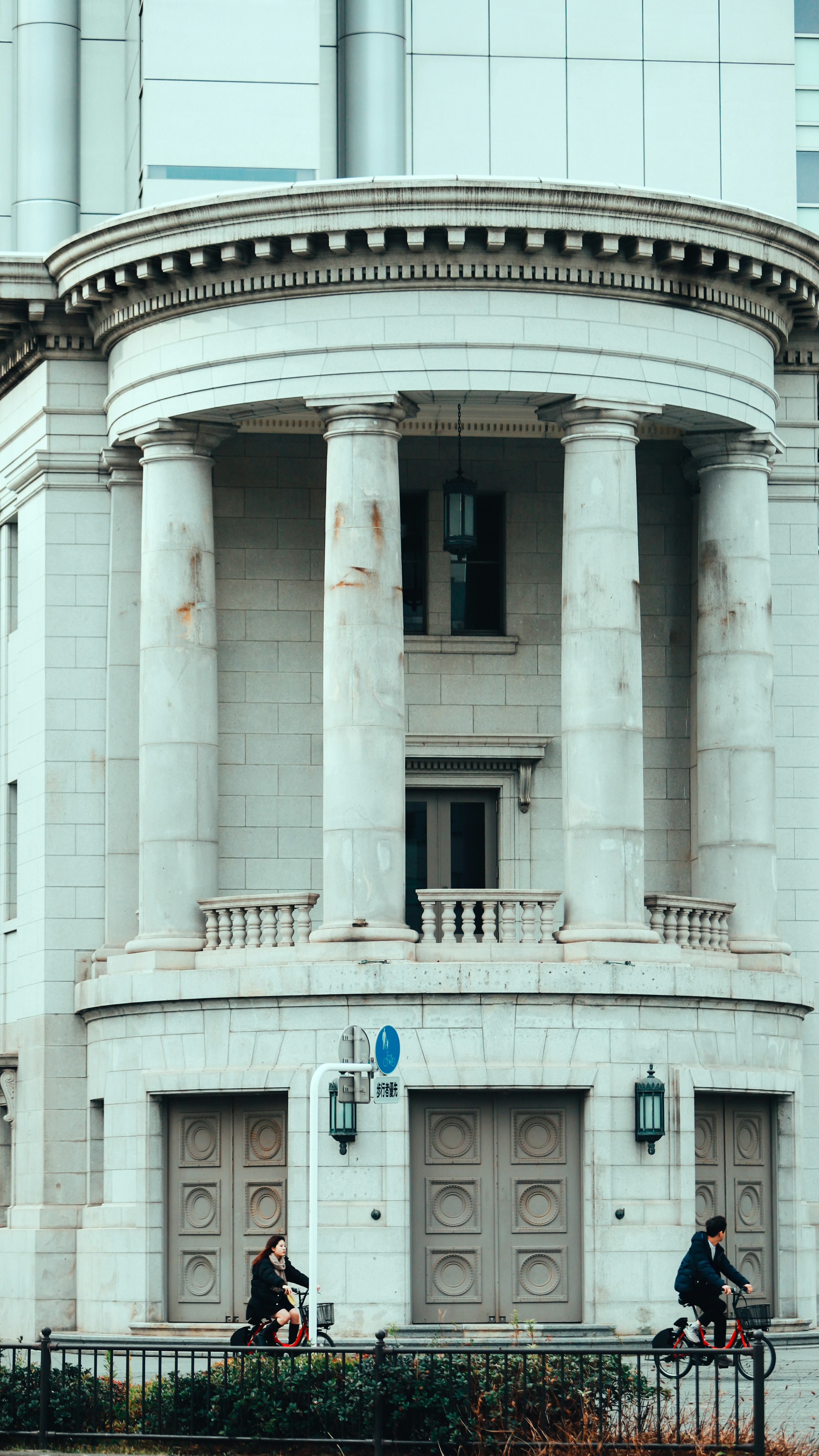 Stone Parade: Two cyclists glide by a grand neoclassical façade