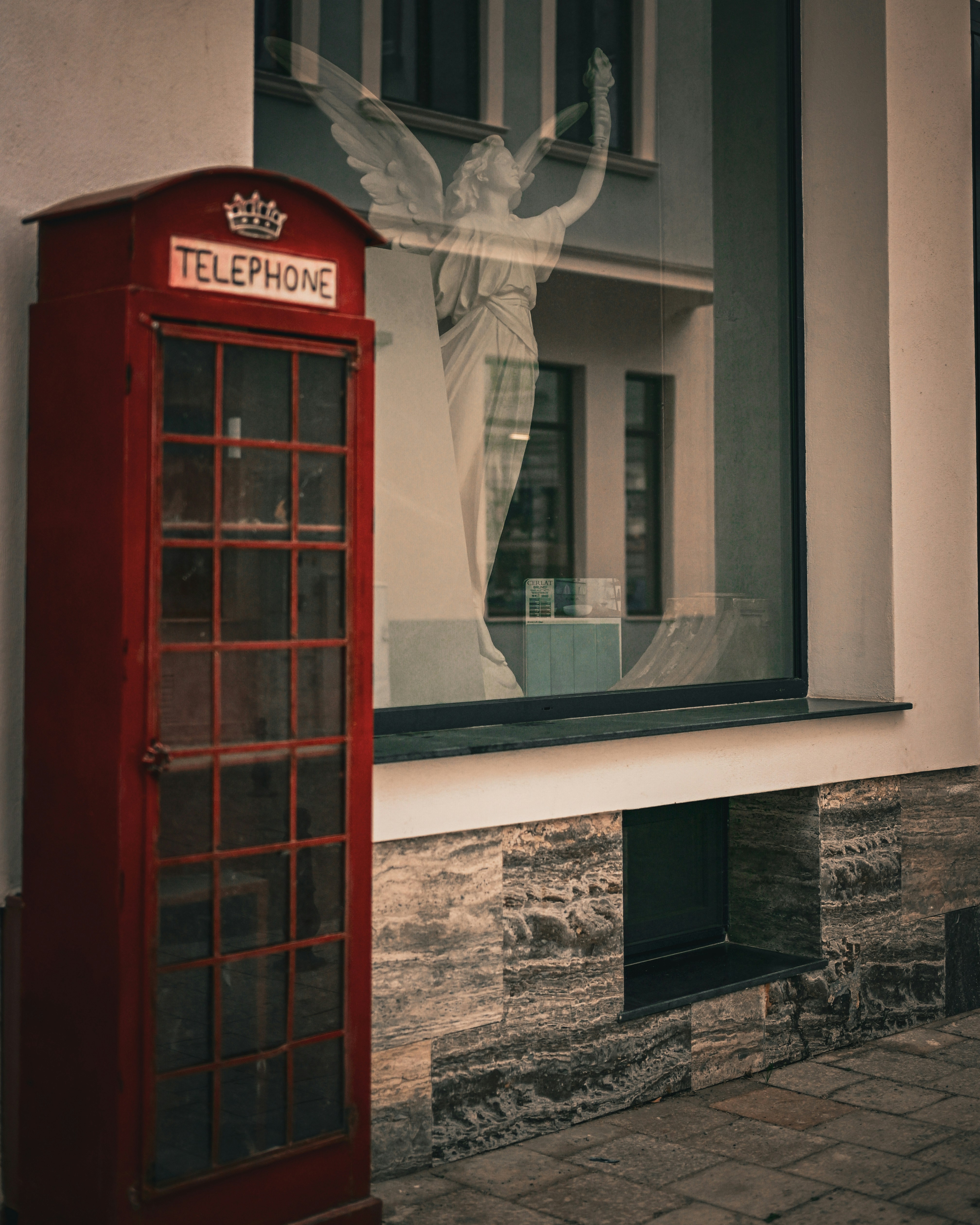 Red Phone Booth by a Ghostly Statue Window