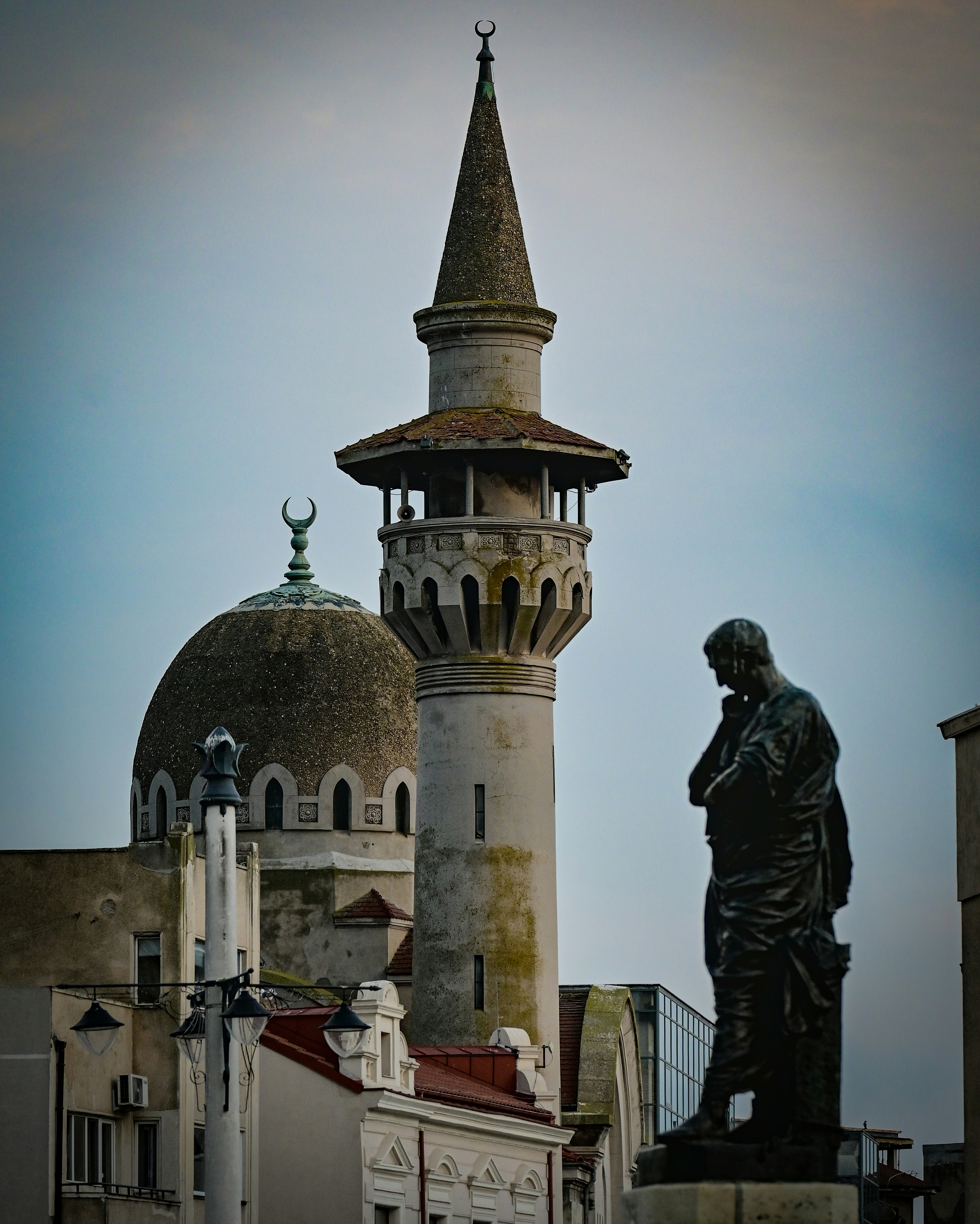 Minaret silhouette over a sunlit cityscape with a solitary statue
