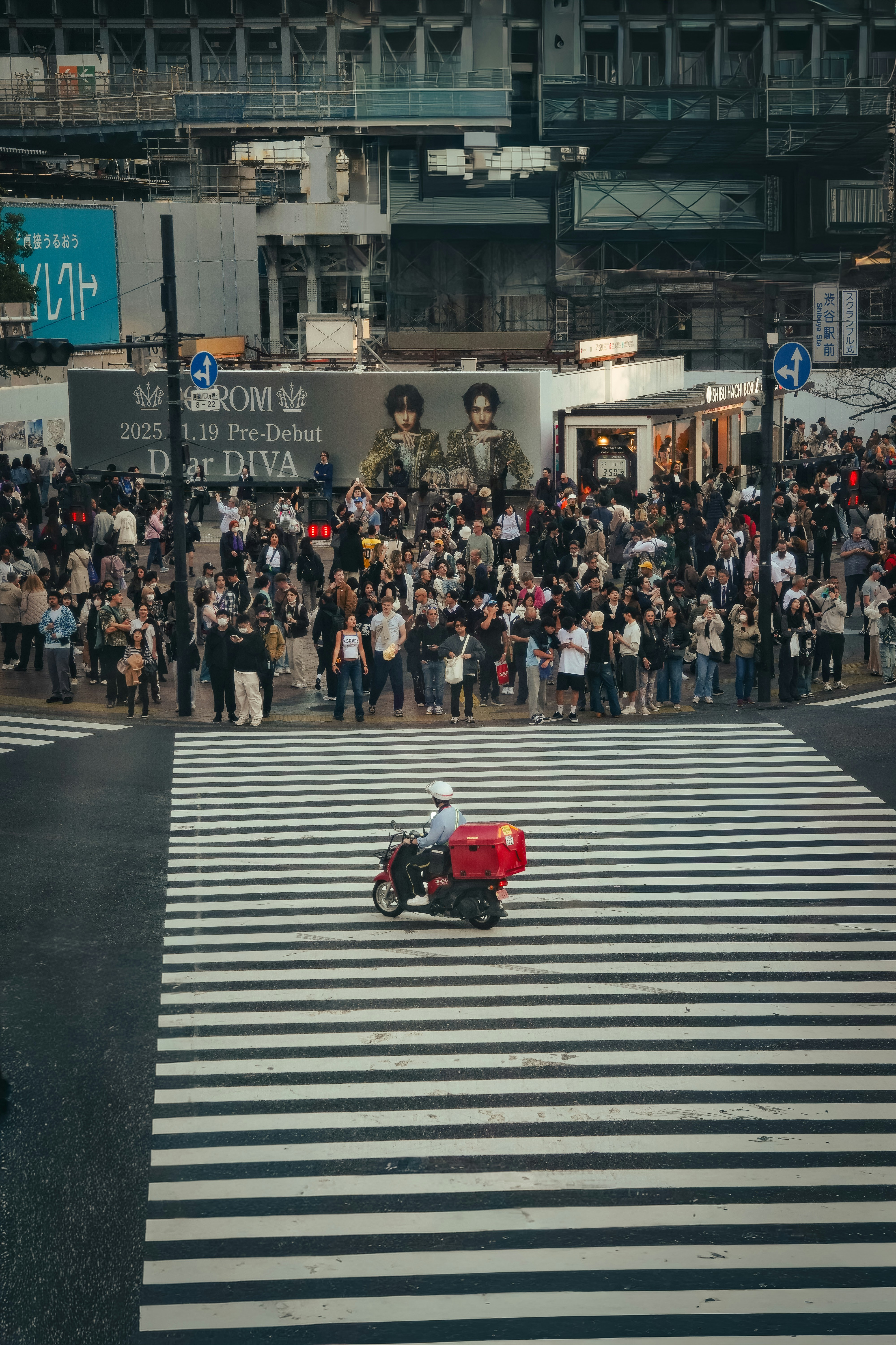 Red Delivery: A lone scooter crosses a bustling urban crosswalk beneath a sea of pedestrians