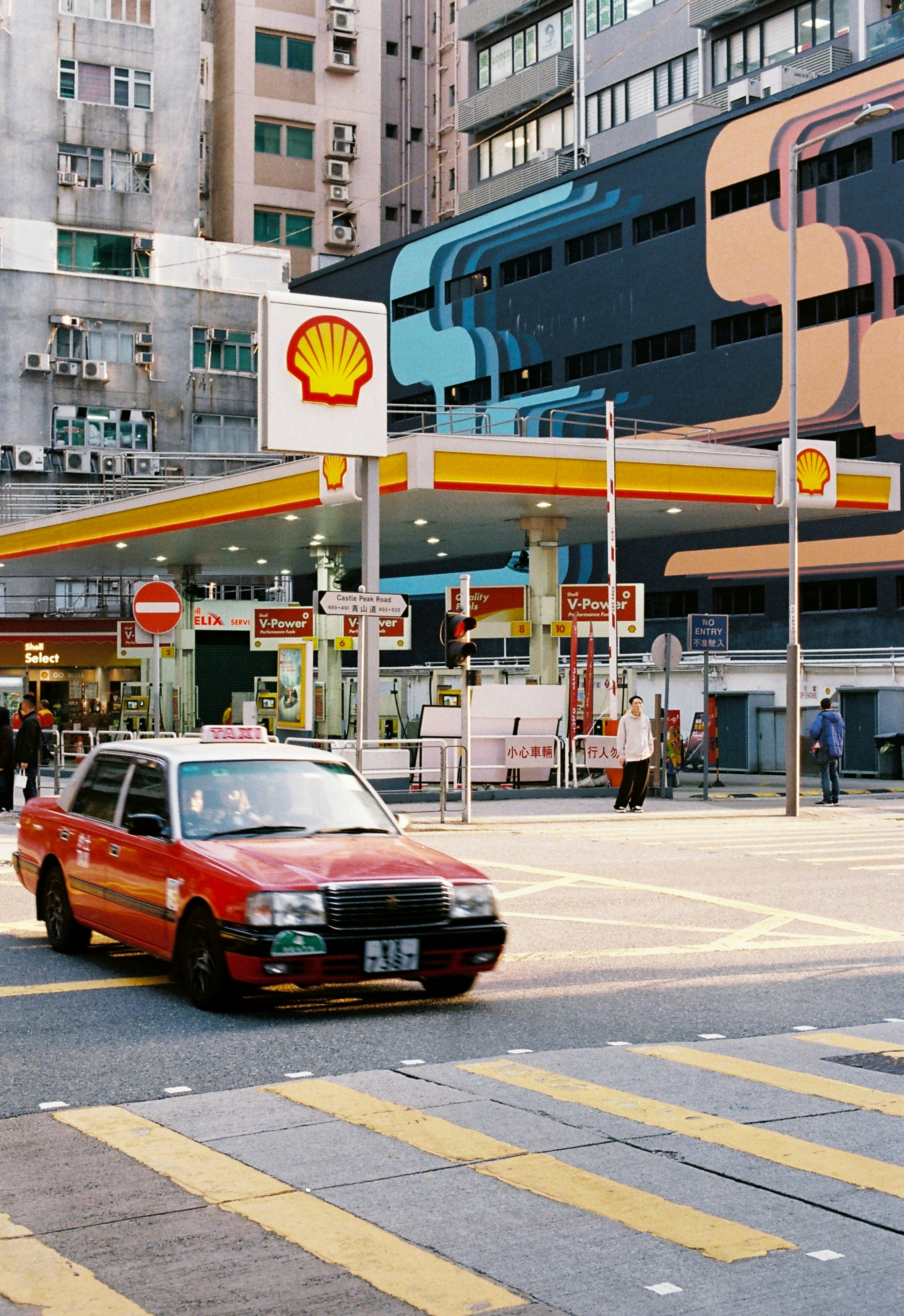 Red taxi drives past a shell gas station in city
