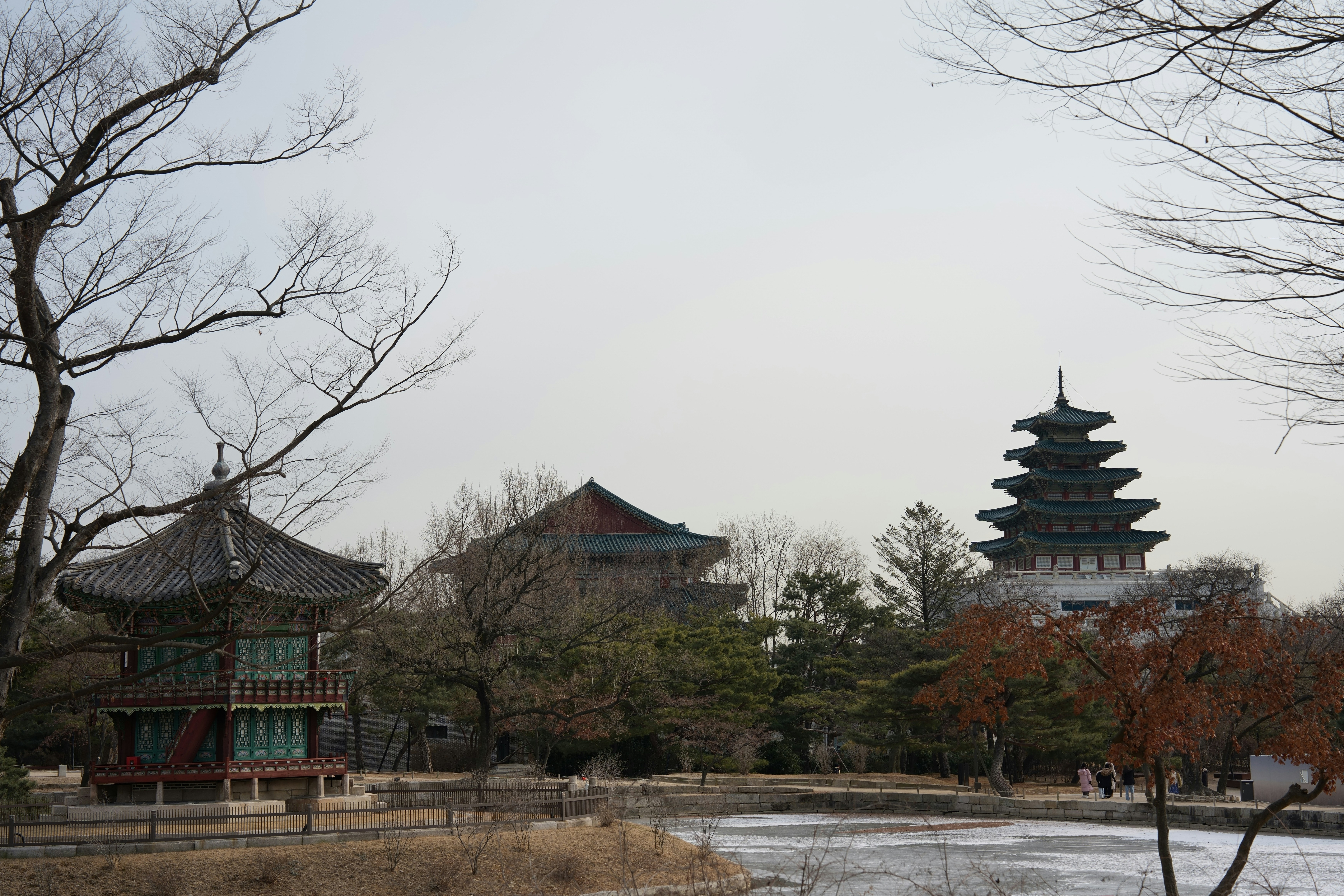 Winter temple grounds with pagoda and pavilion framed by bare trees and a calm, pale sky.