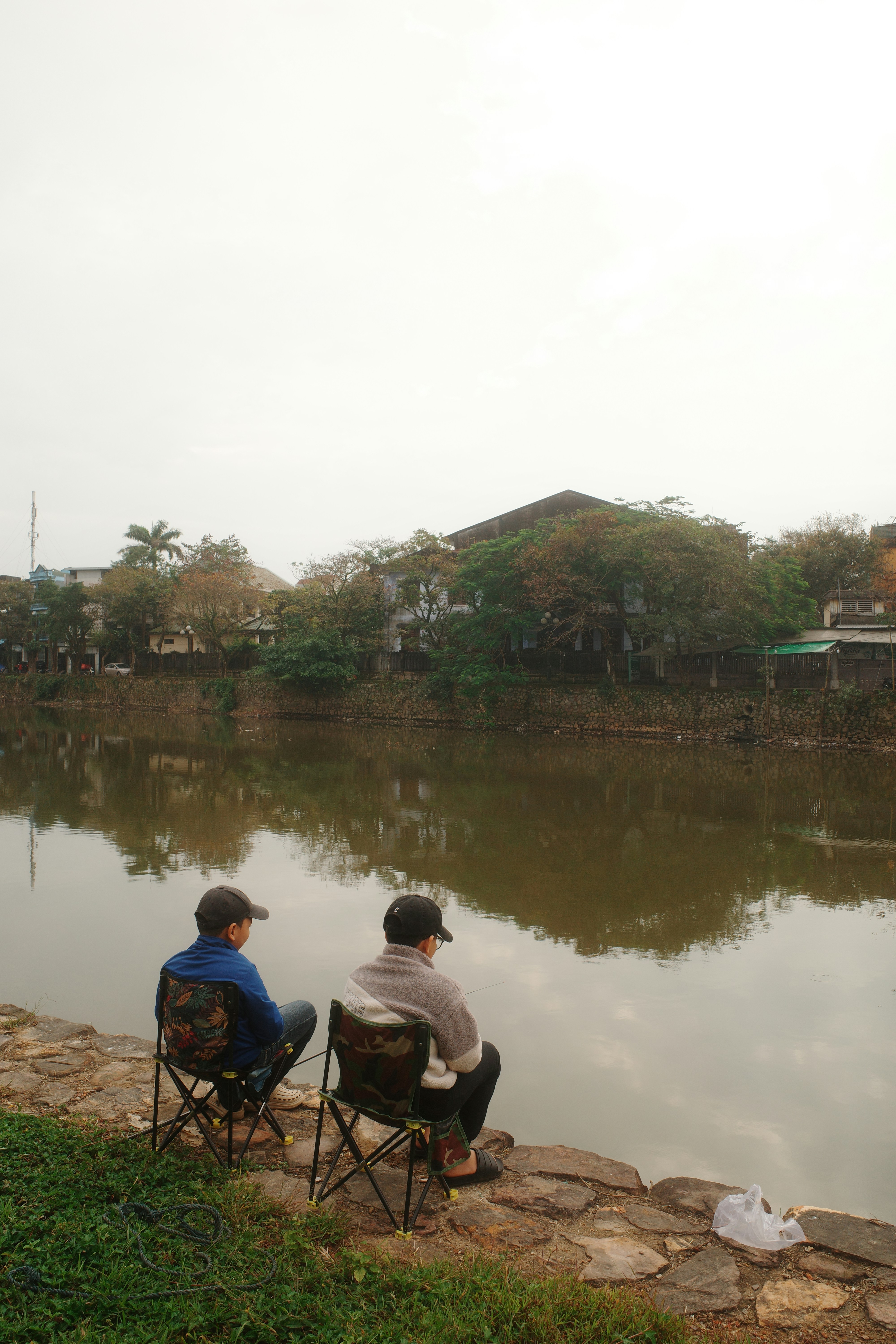 Two anglers by a calm riverside, captured at dusk