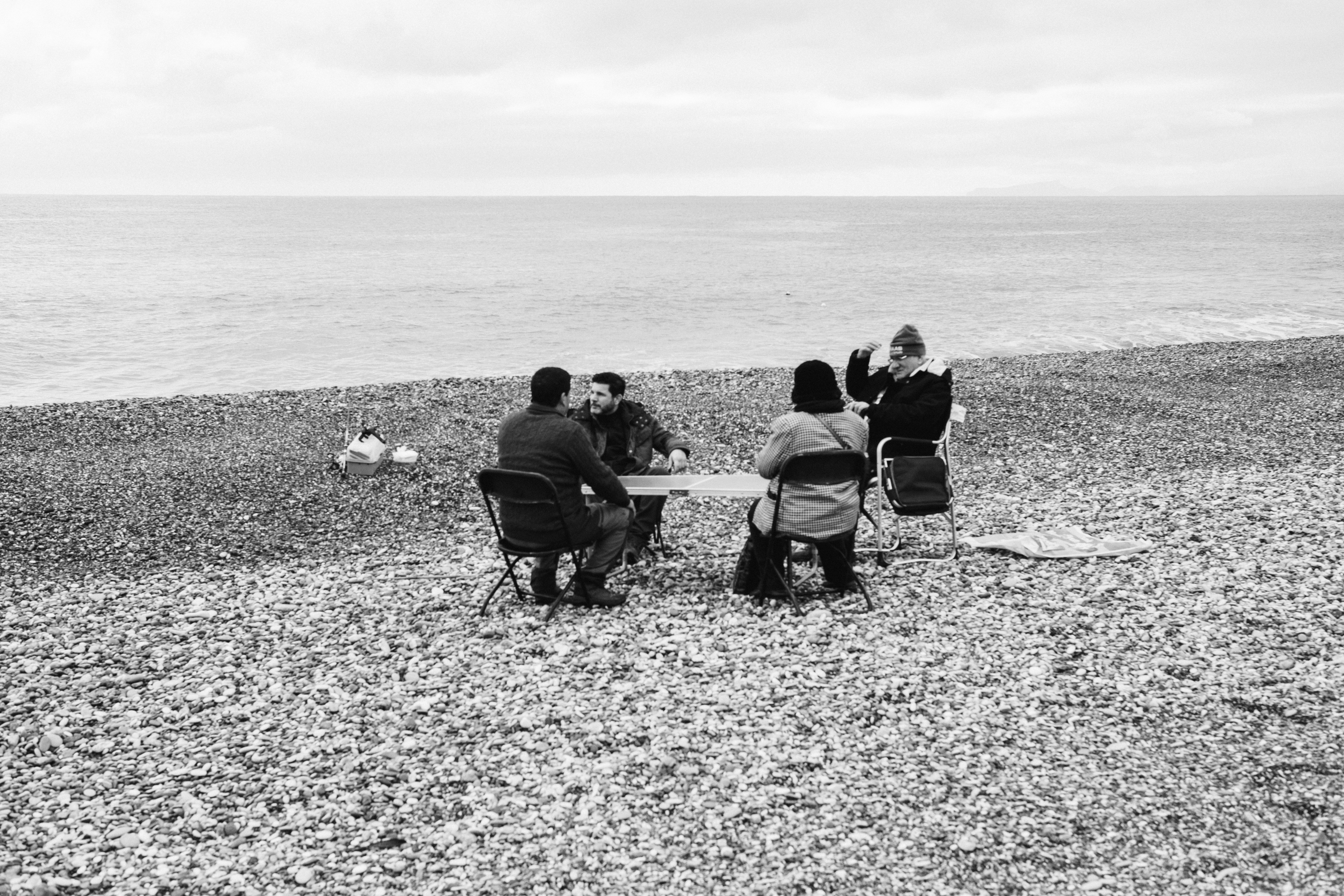 People gathered at a table on a pebble beach
