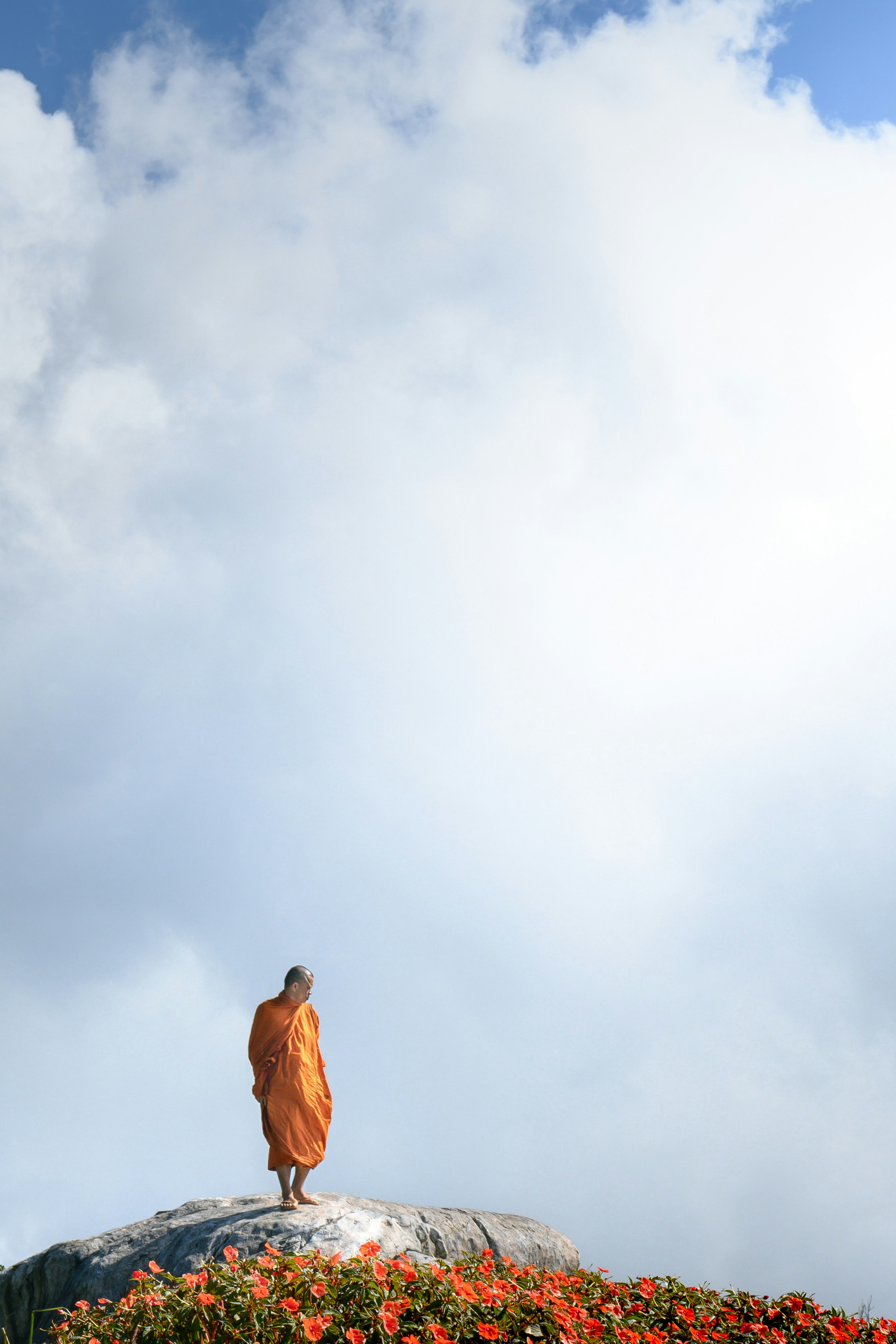 Monk in Orange Robe Standing on Rock Against Expansive Sky