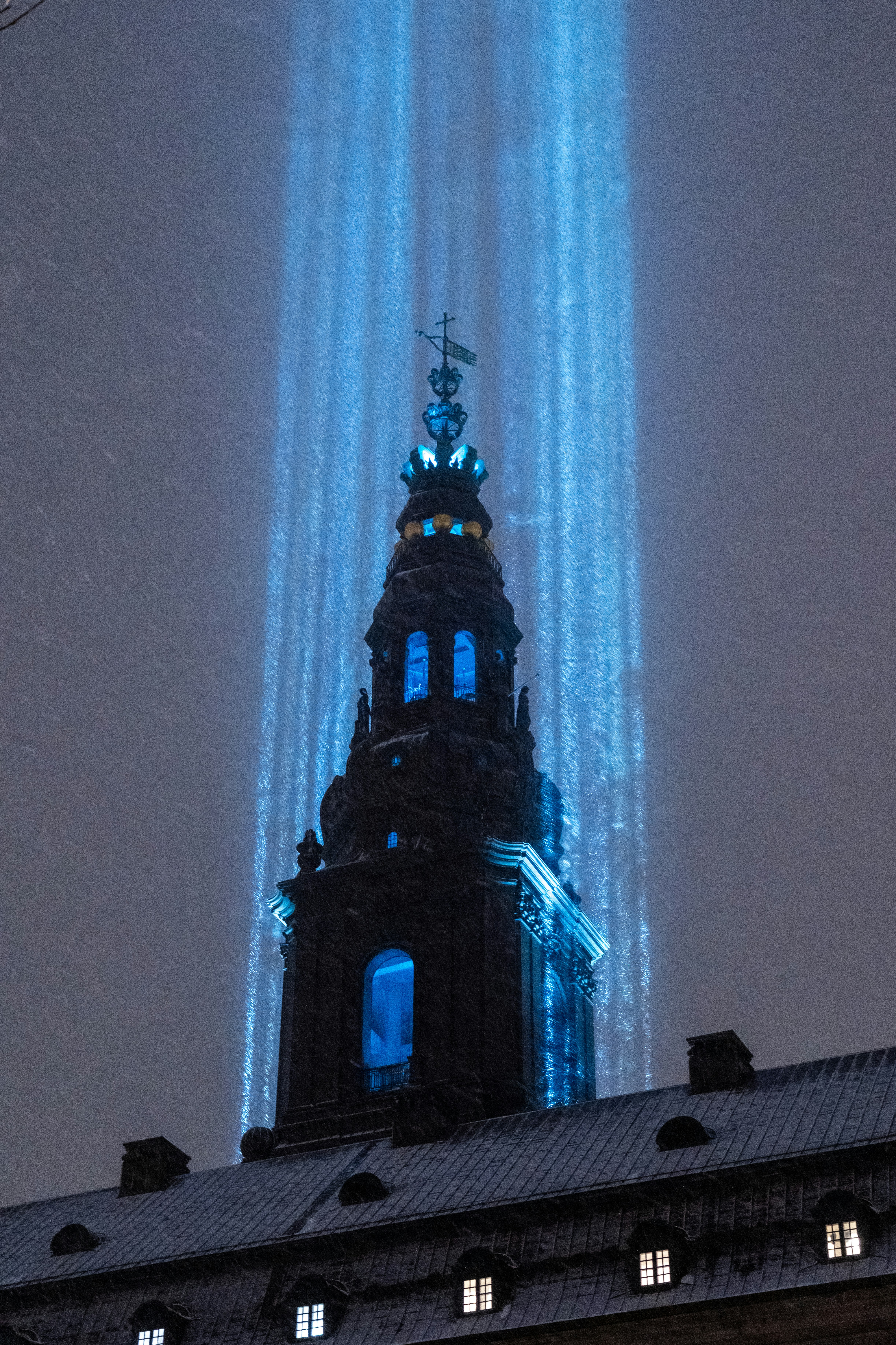 Vertical blue light columns crown a historic spire
