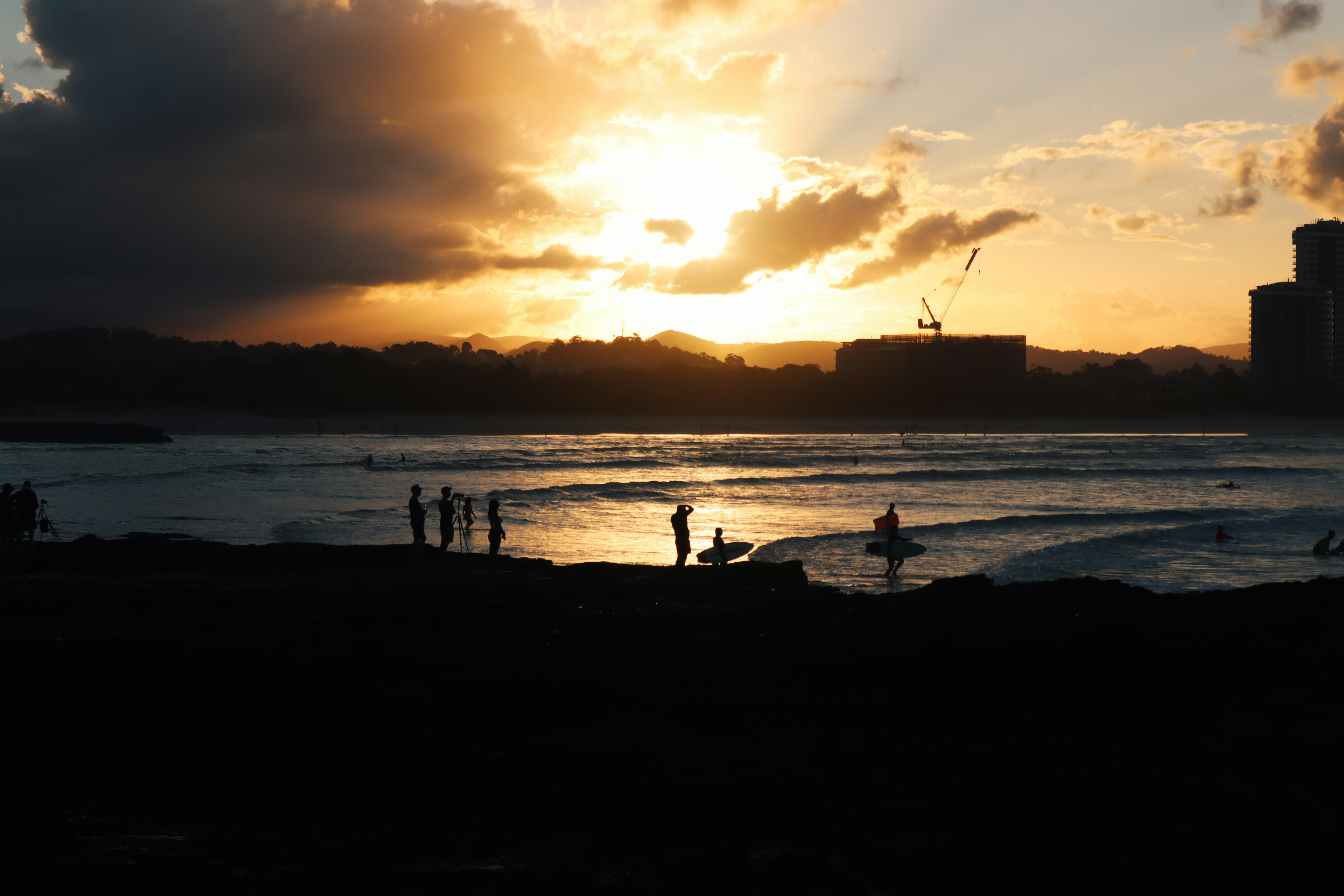 Sunset silhouettes on the shoreline as harbor lights awaken