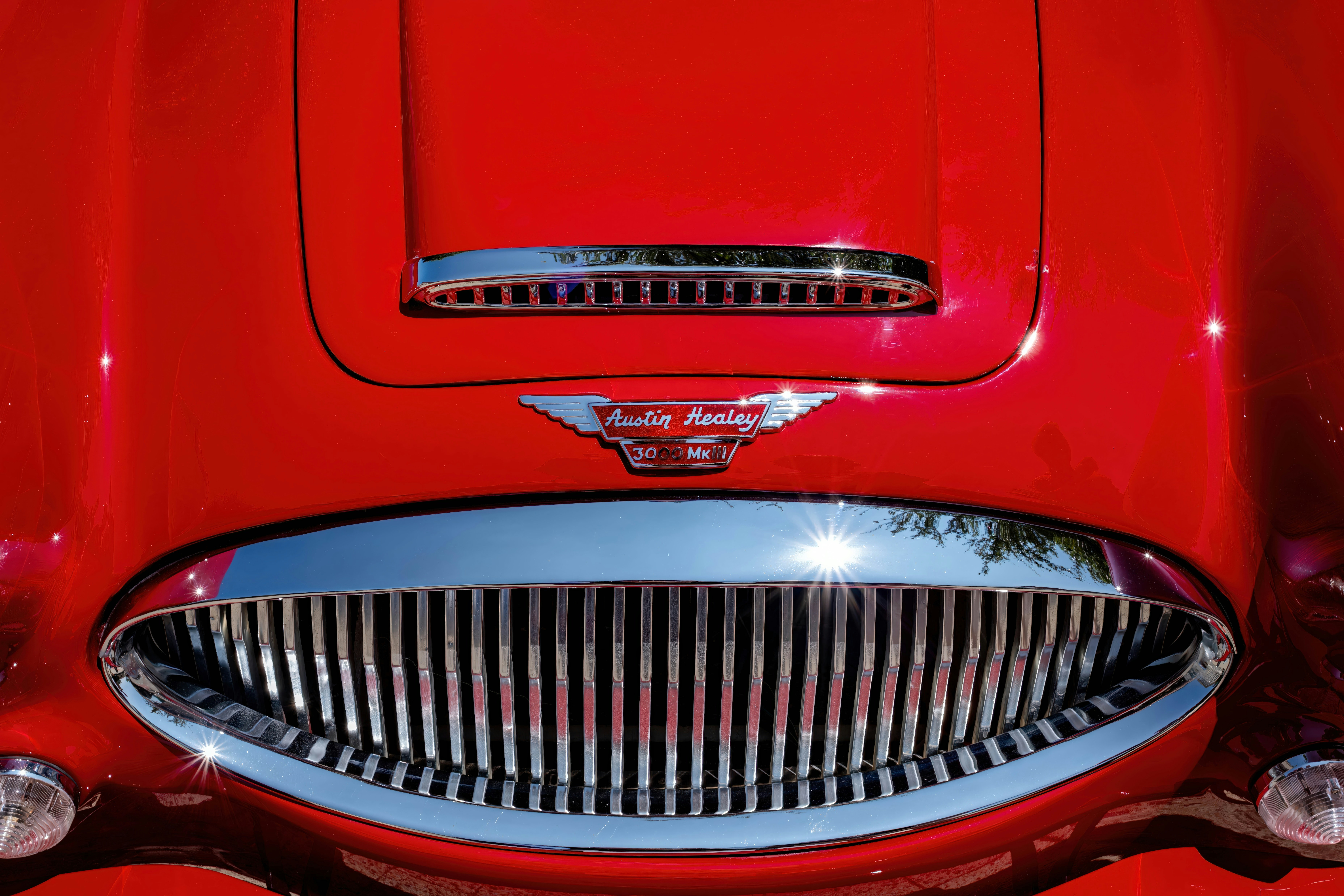 A gleaming grille of heritage: Austin-Healey emblem on cherry red chrome