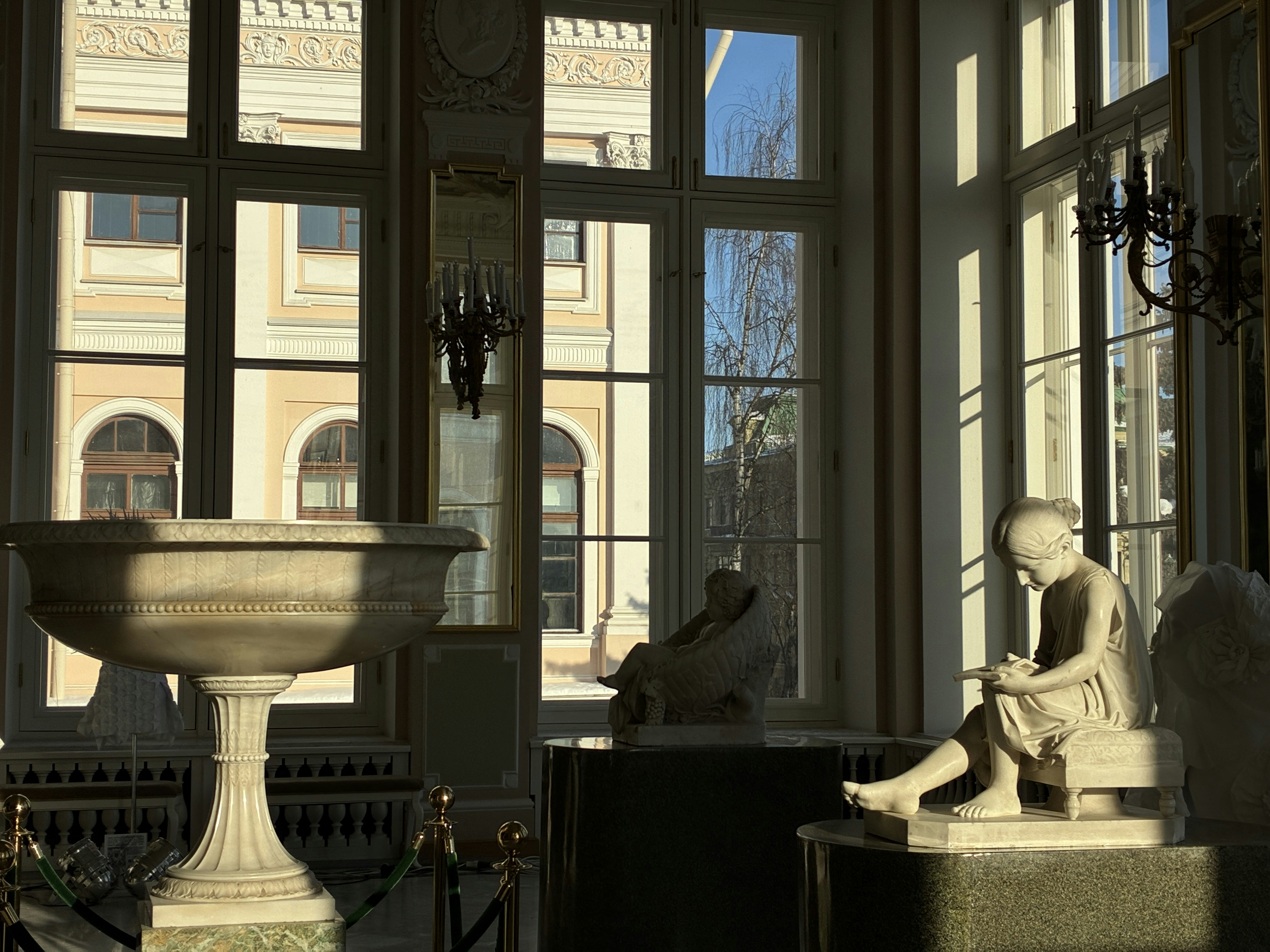 Sunlit room with marble sculptures and large windows.