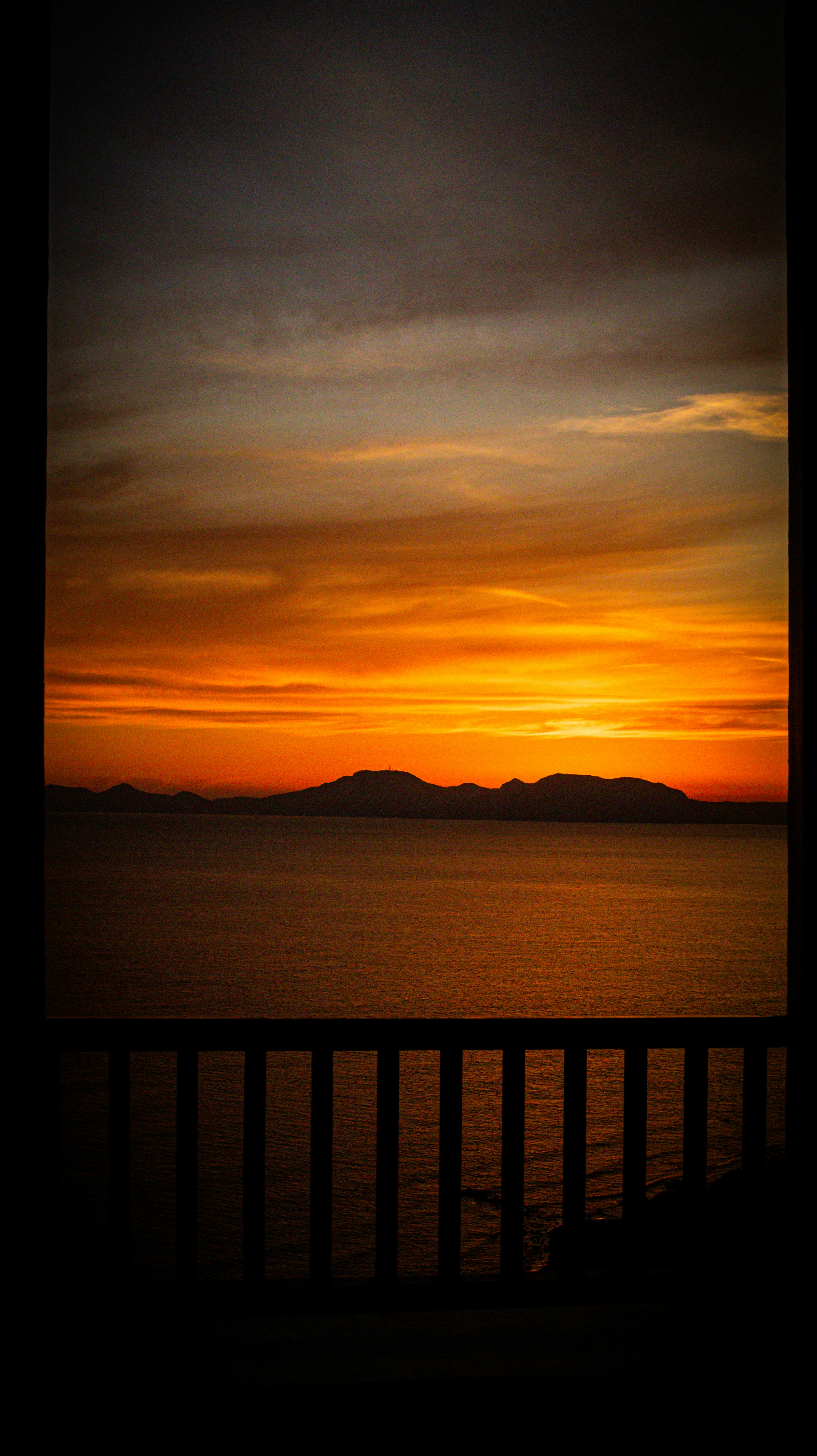Sunset Over Quiet Waters: A silhouetted railing frames a fiery horizon