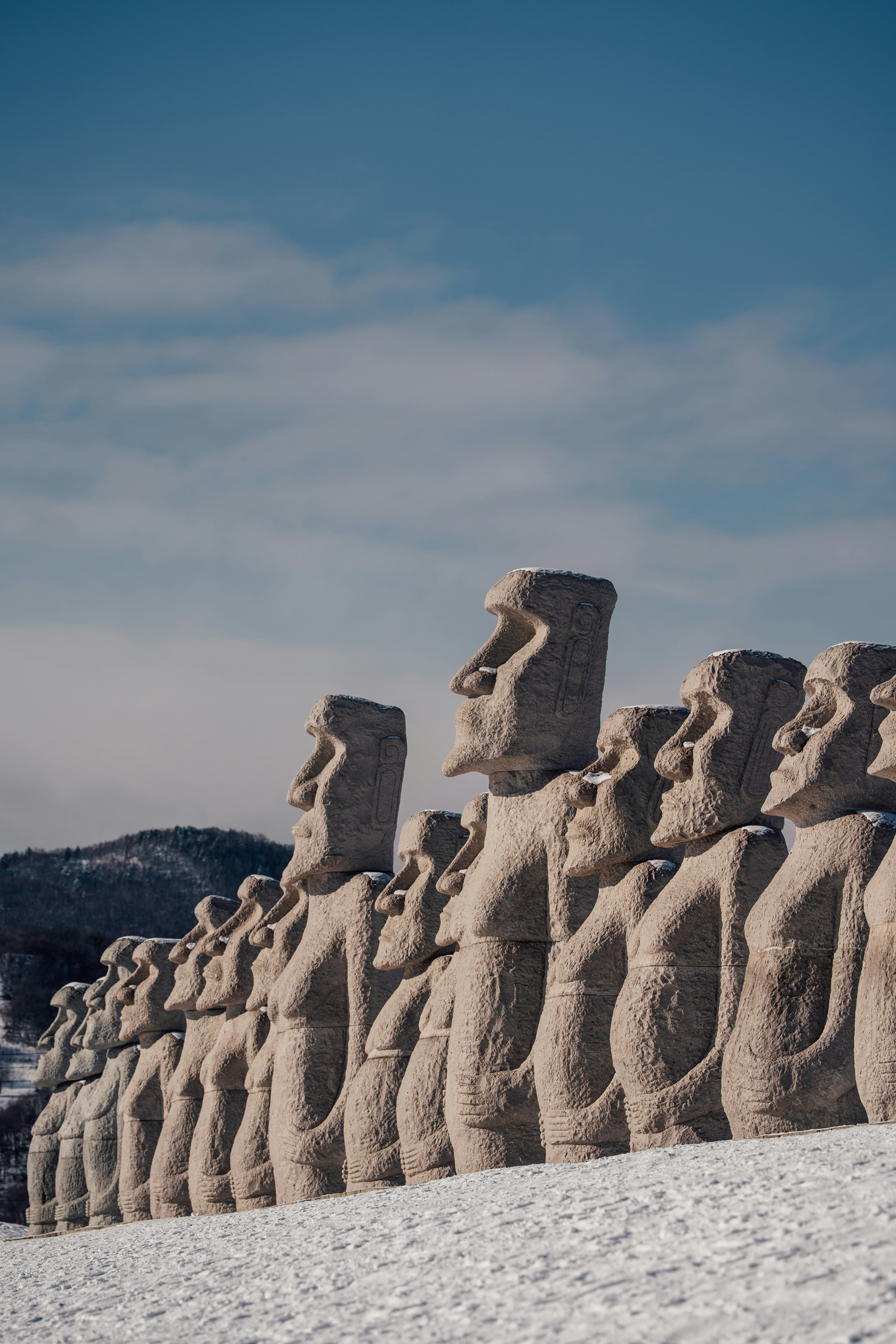 Row of Moai-like Stone Figures Standing Against Snow and Blue Sky
