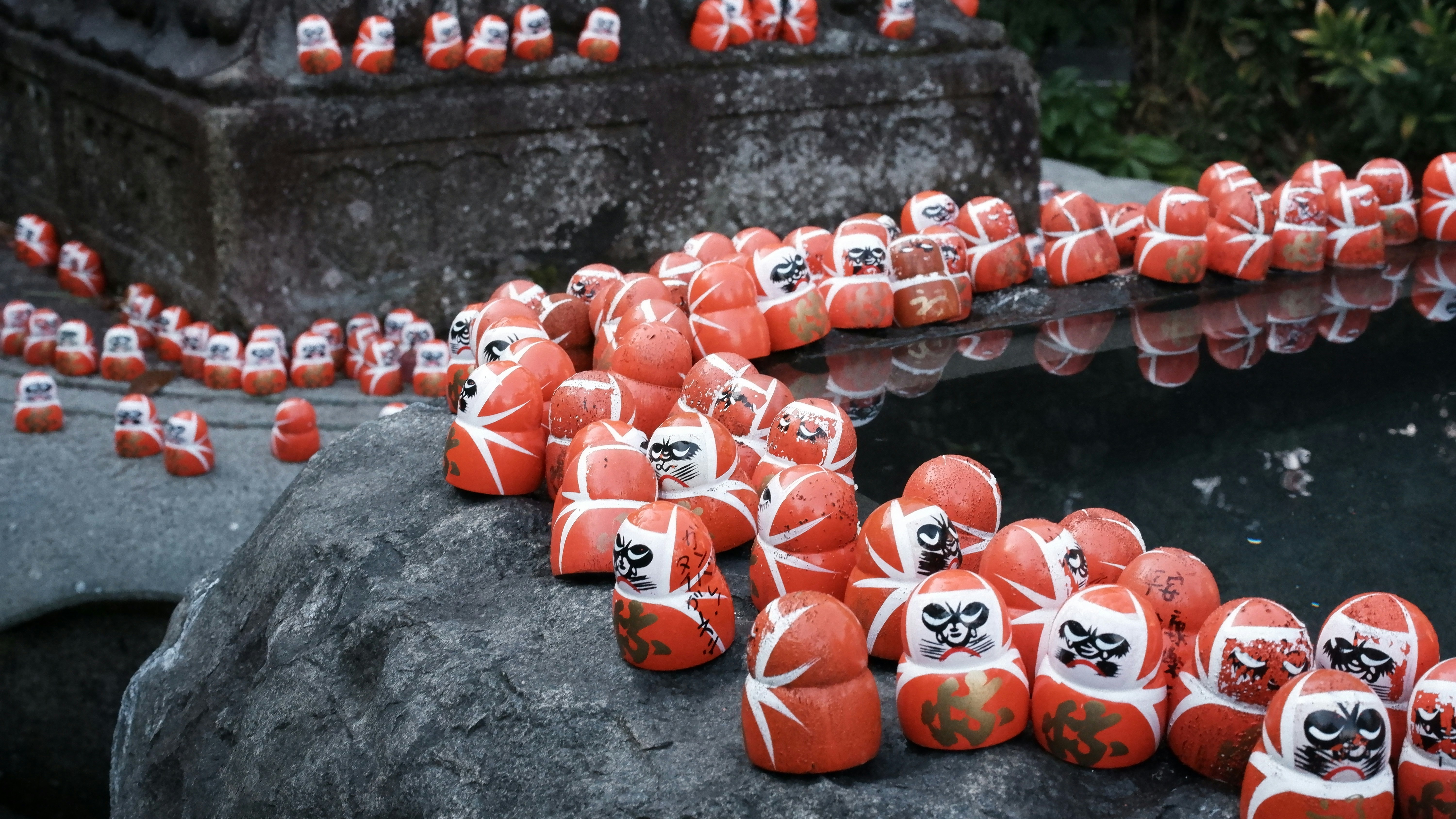 Row of carved orange daruma statues draped along a reflective pond edge