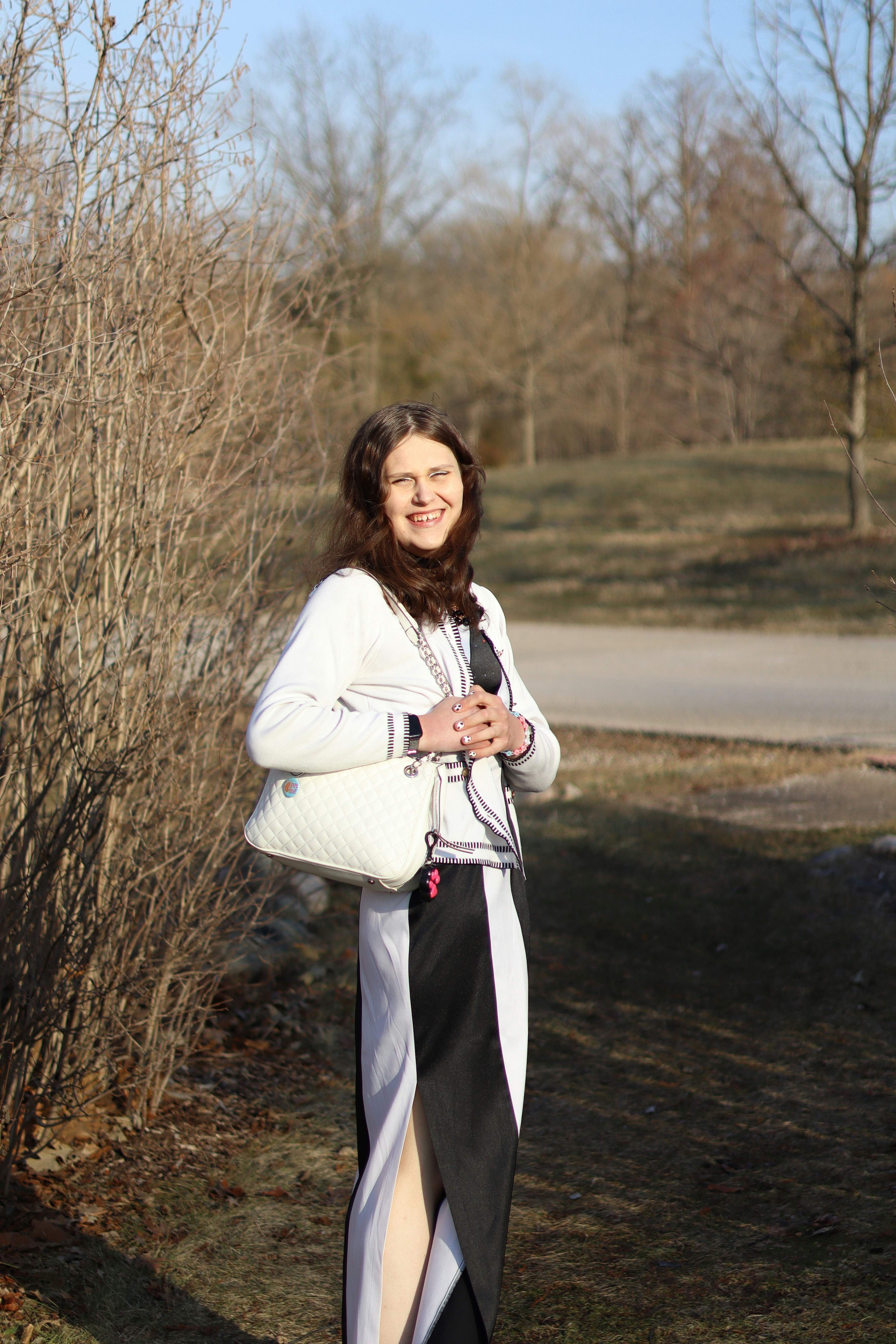 Sunlit confidant: a woman in white beside a hedge on a crisp day