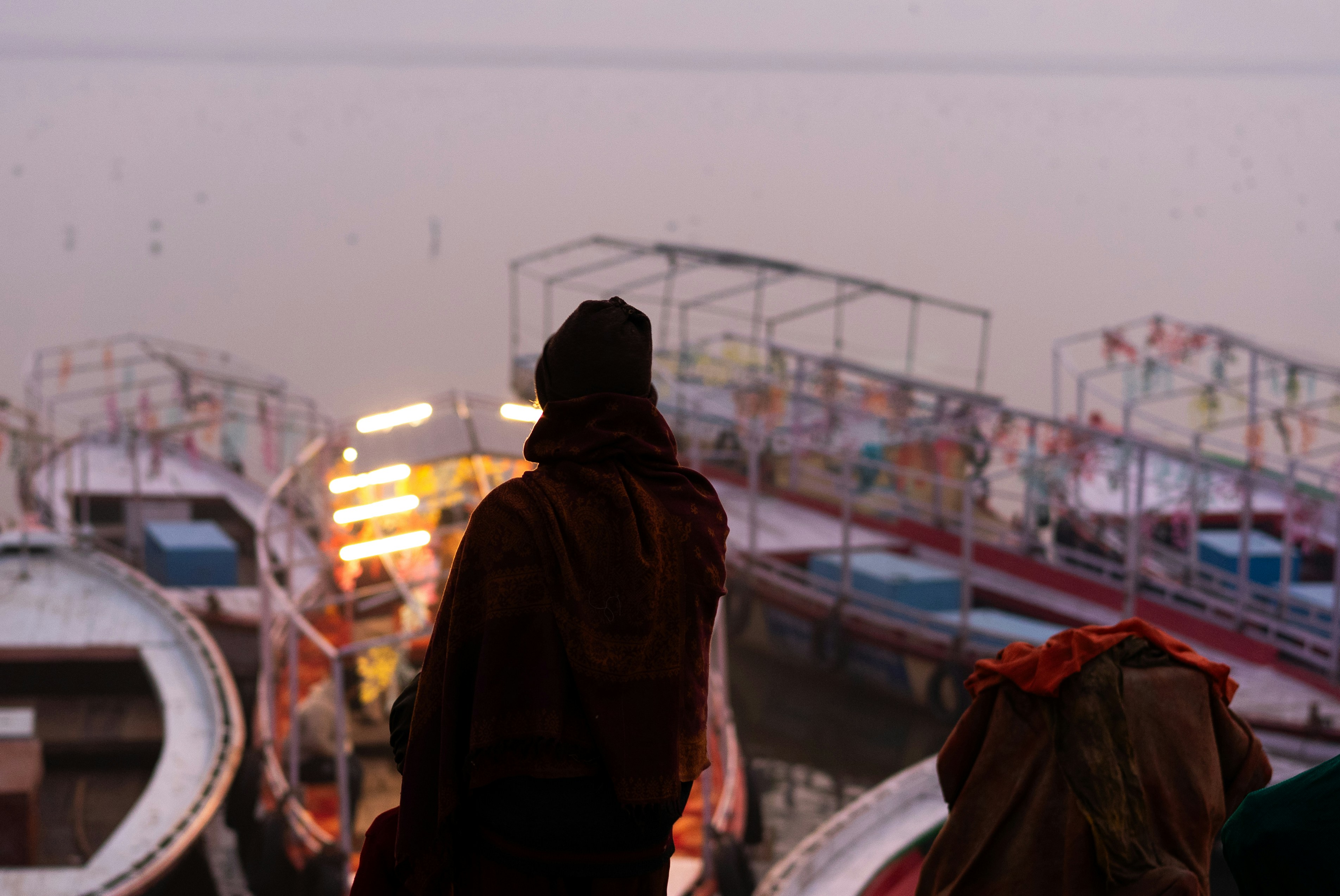 Hooded silhouette overlooking a canopy of rides by the harbor