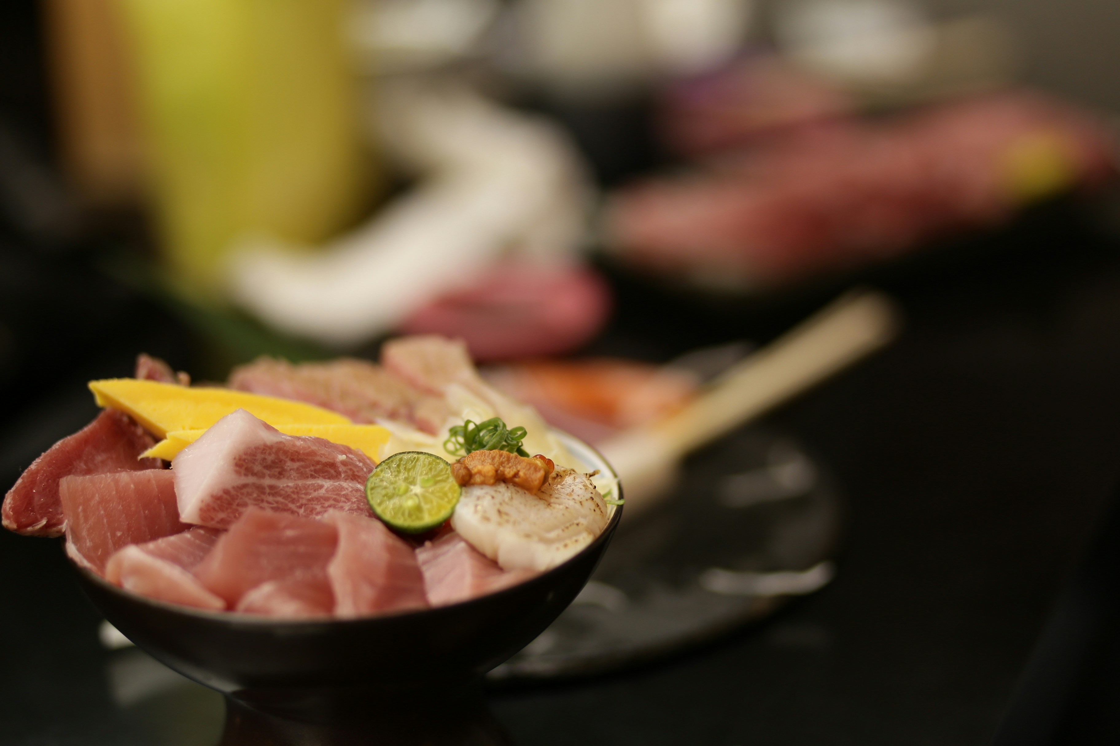 Bowl of vibrant sashimi with citrus and garnish on a dim restaurant counter