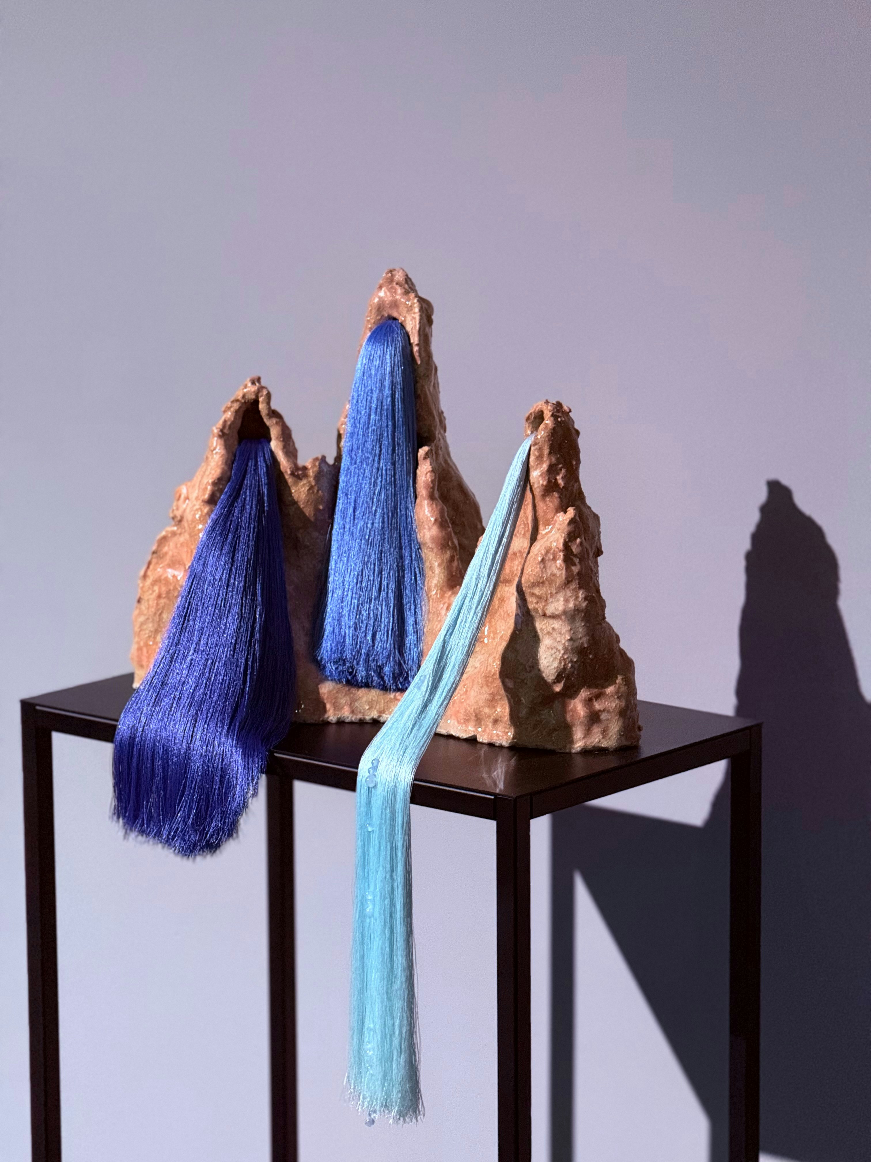 Three cobalt tresses on a rocky pedestal with a shadowed silhouette