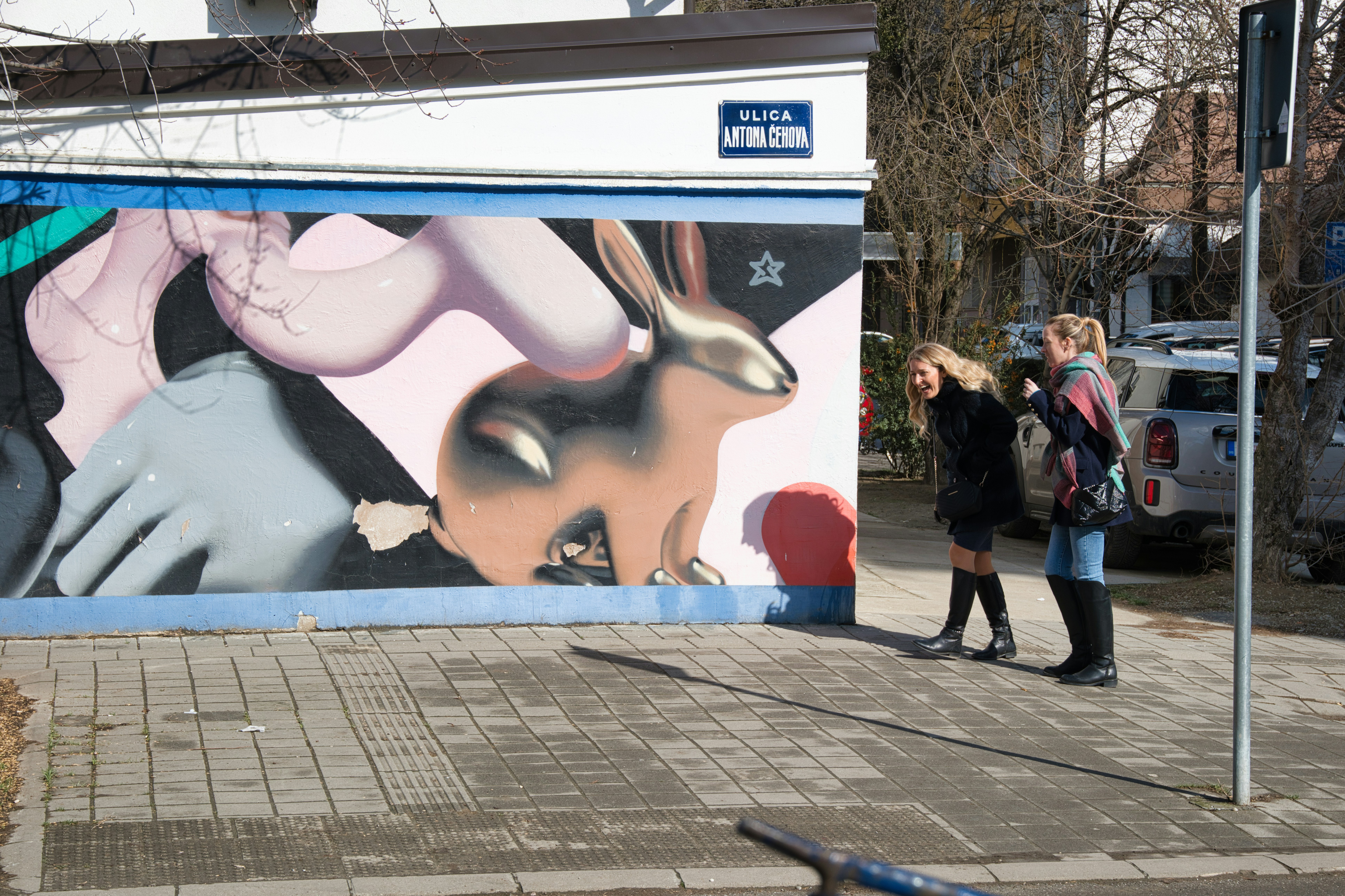 Faces in Transit: Two passersby beside a mural under urban daylight