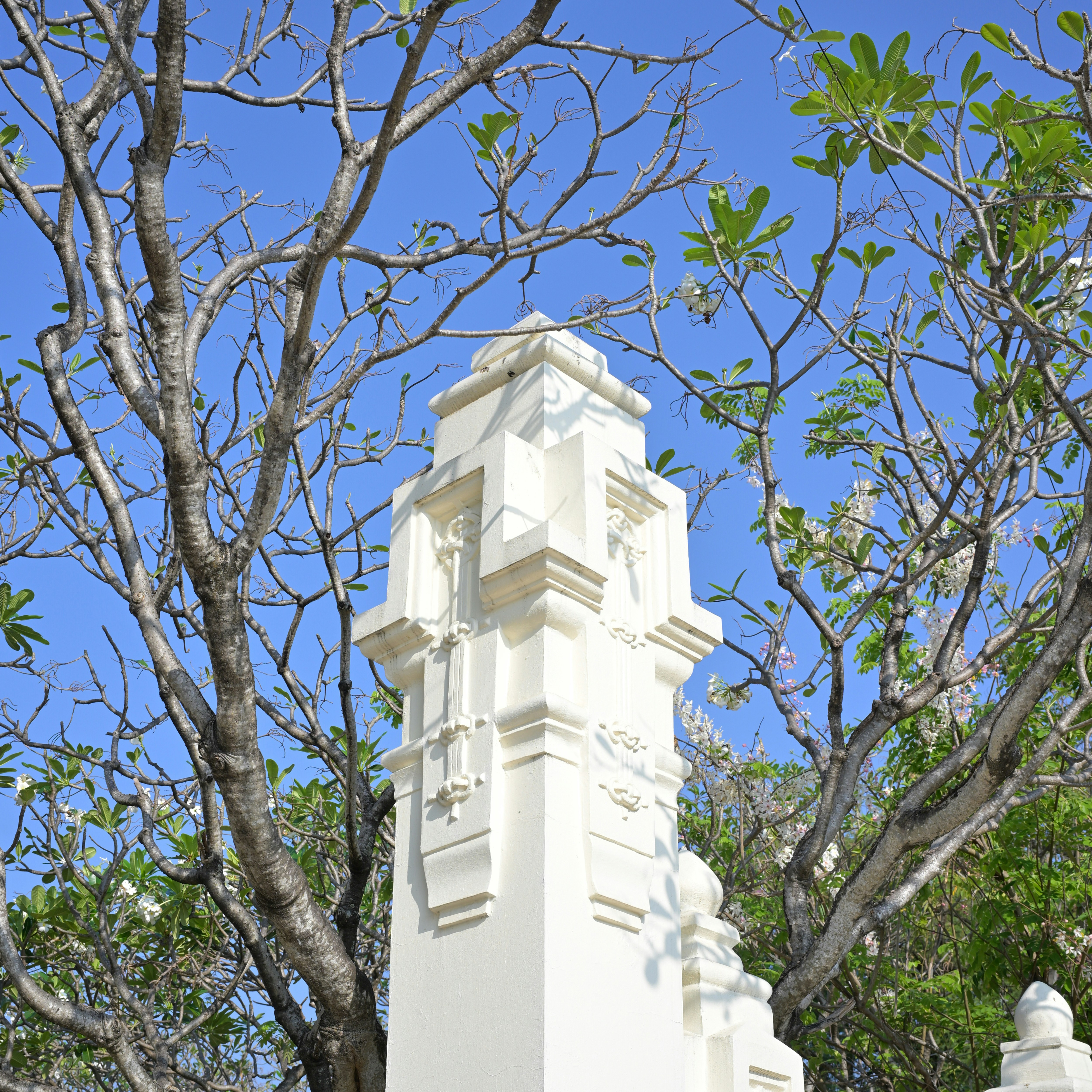White Monument Framed by Leafy Branches Under Clear Blue Sky