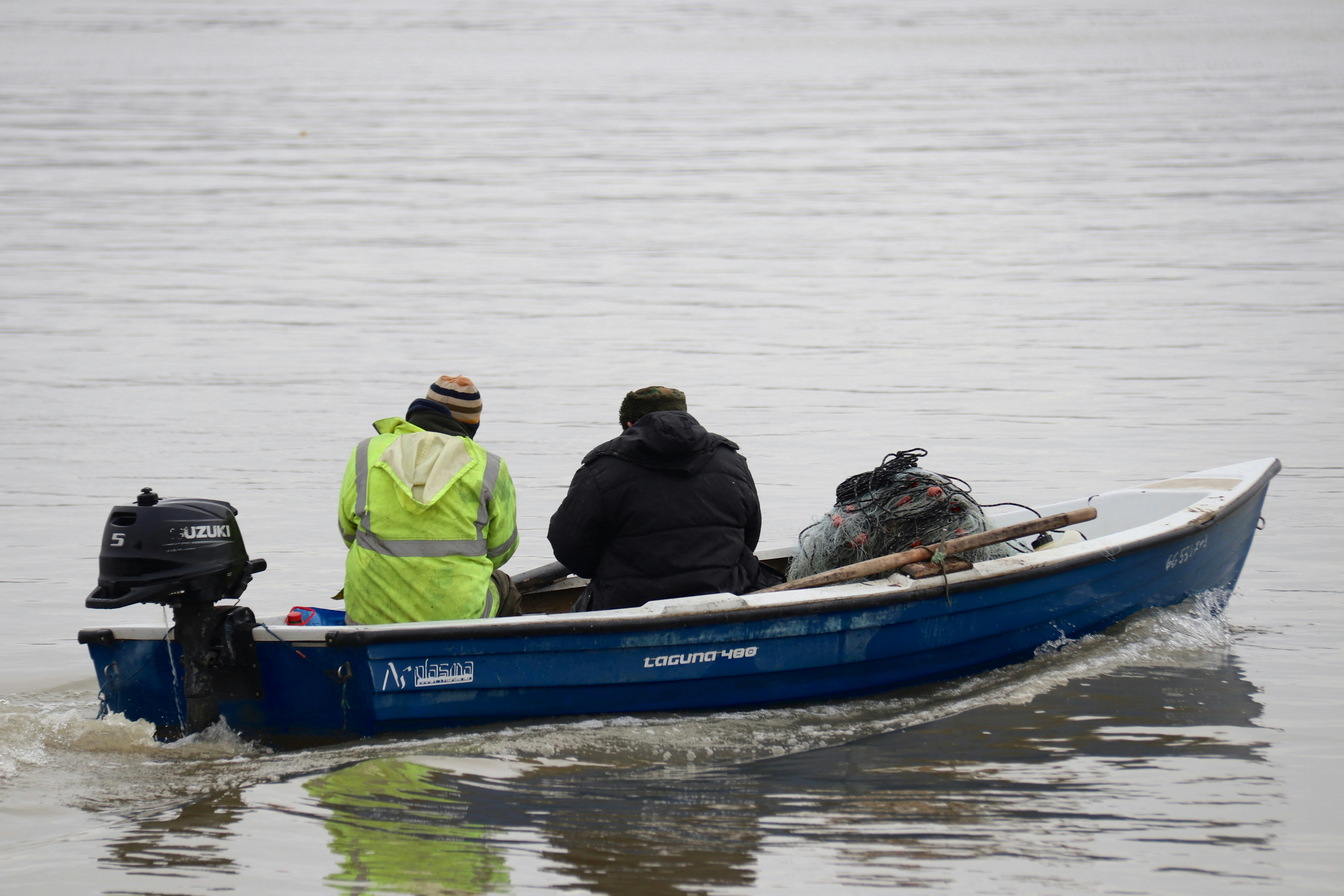Two boatmen in a blue workboat navigating calm harbor waters