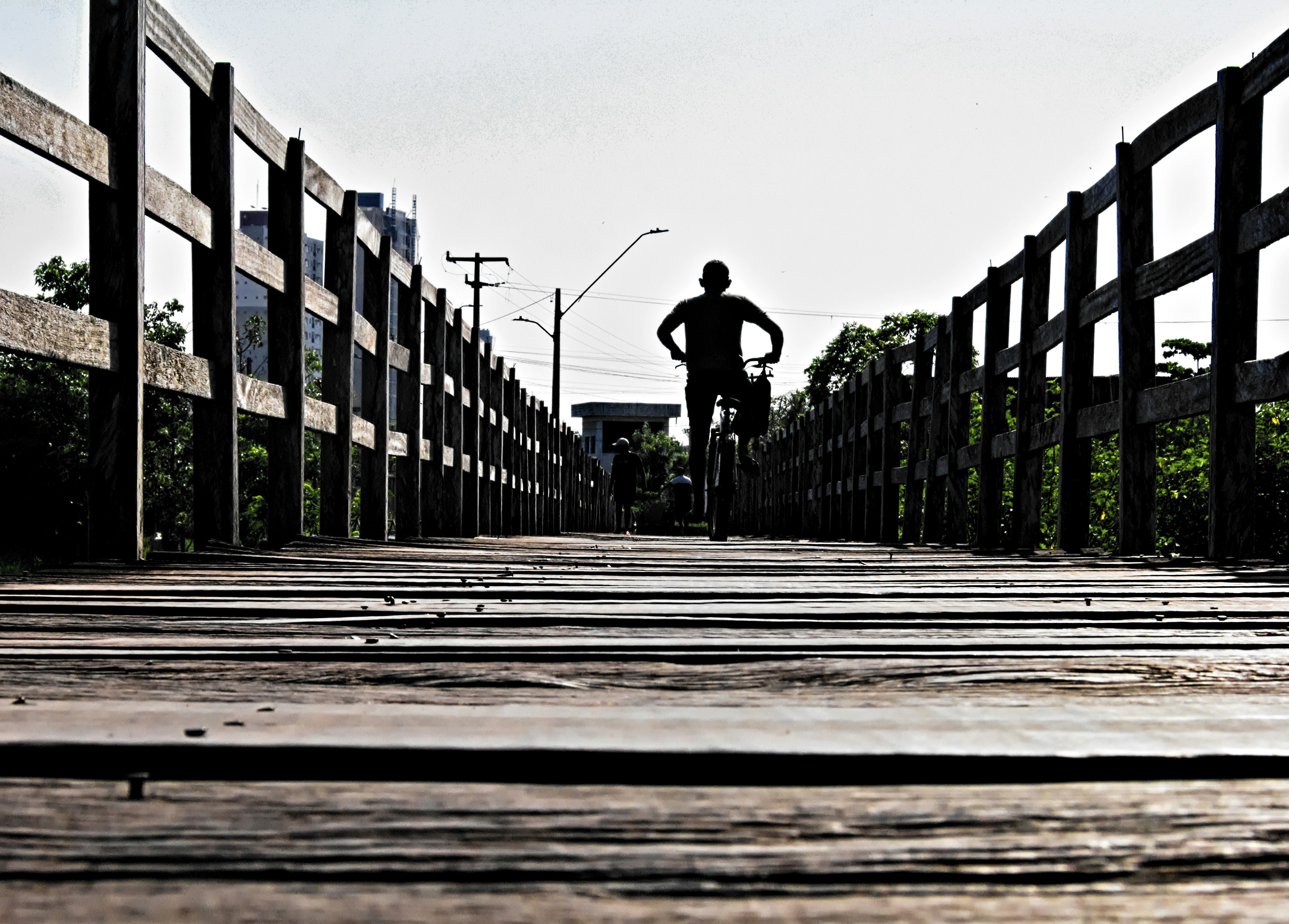 Silhouette of a person cycling on a wooden bridge.