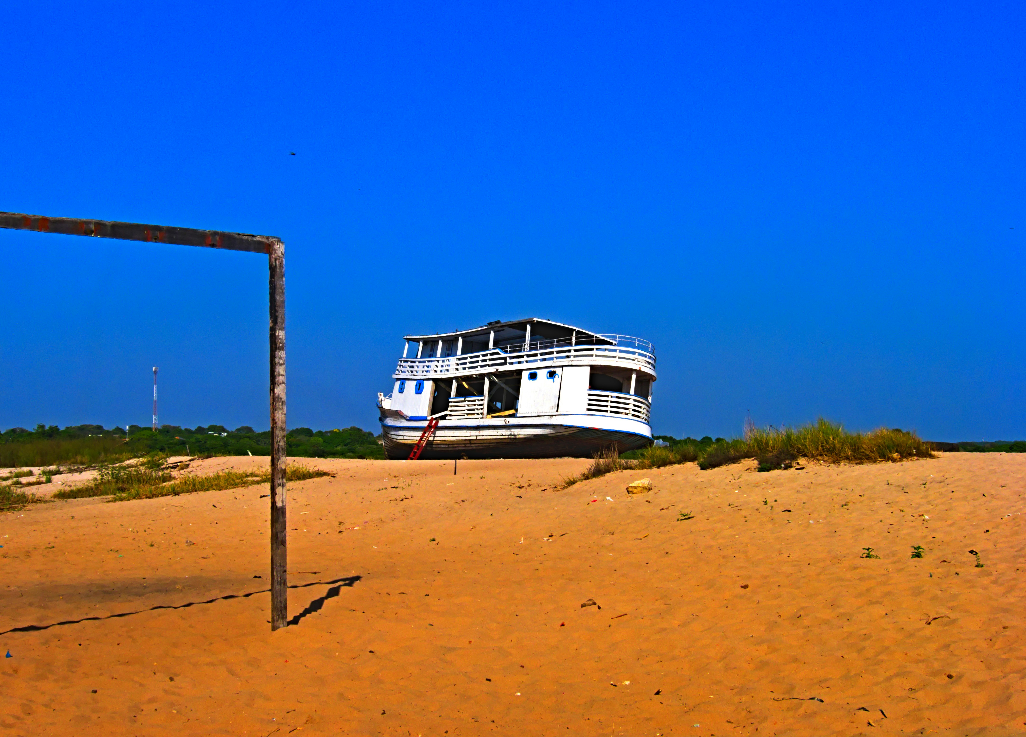 A boat lies in the middle of the bush and the vines, bushes and sand. The river is dry.