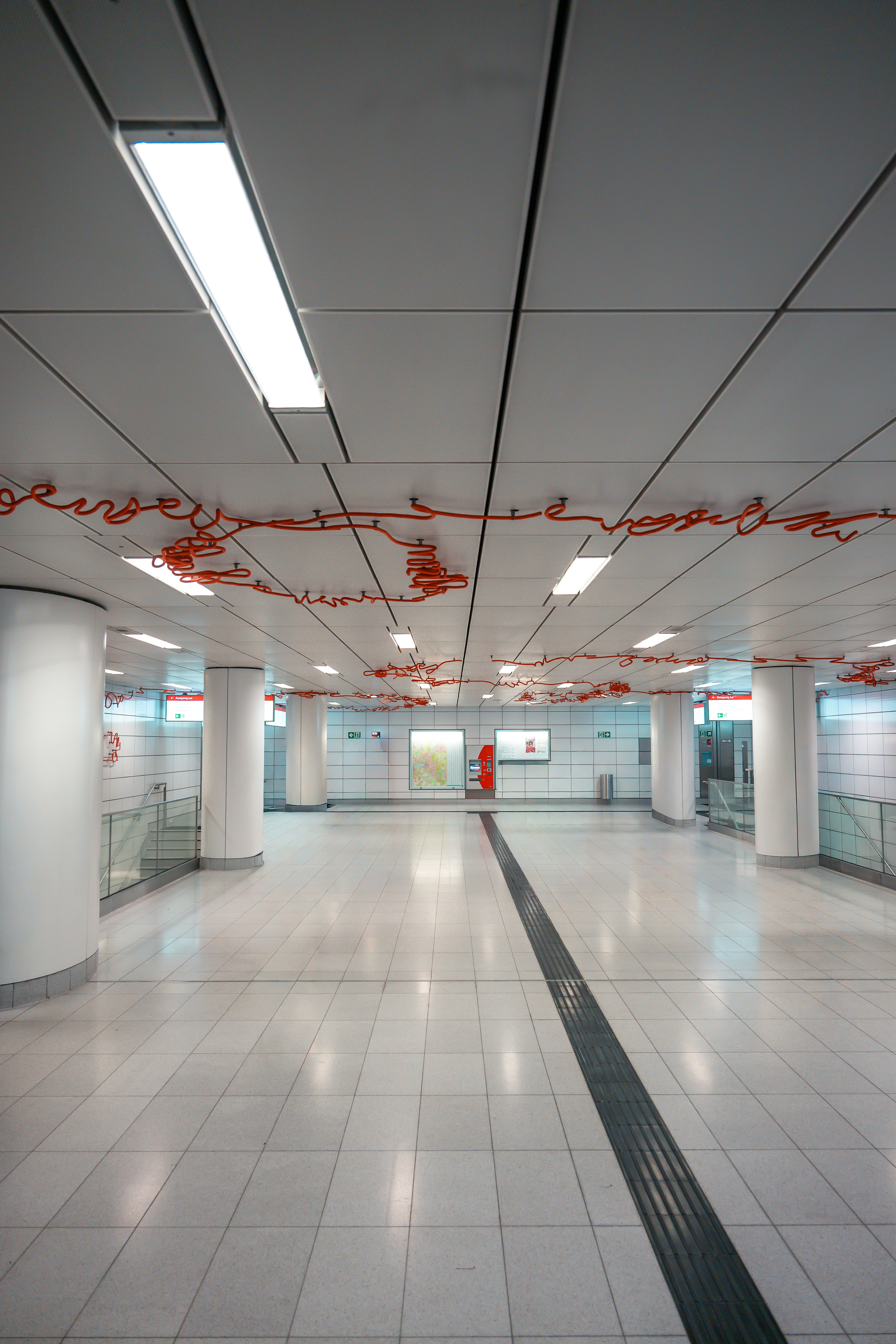 Red Script Over Aisles: A Quiet Subway Atrium