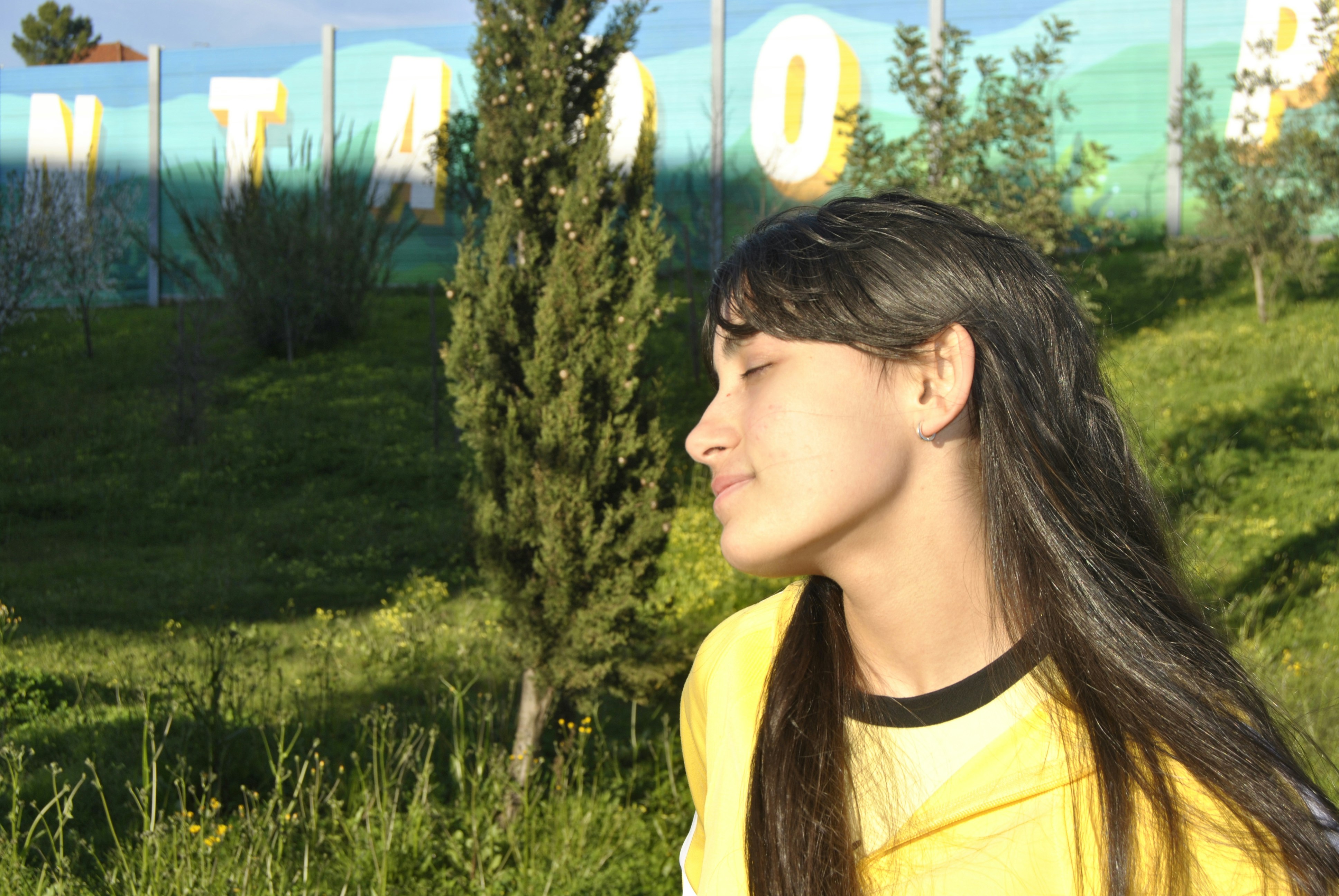 Sunlit Profile: a girl in a yellow shirt against a mural backdrop