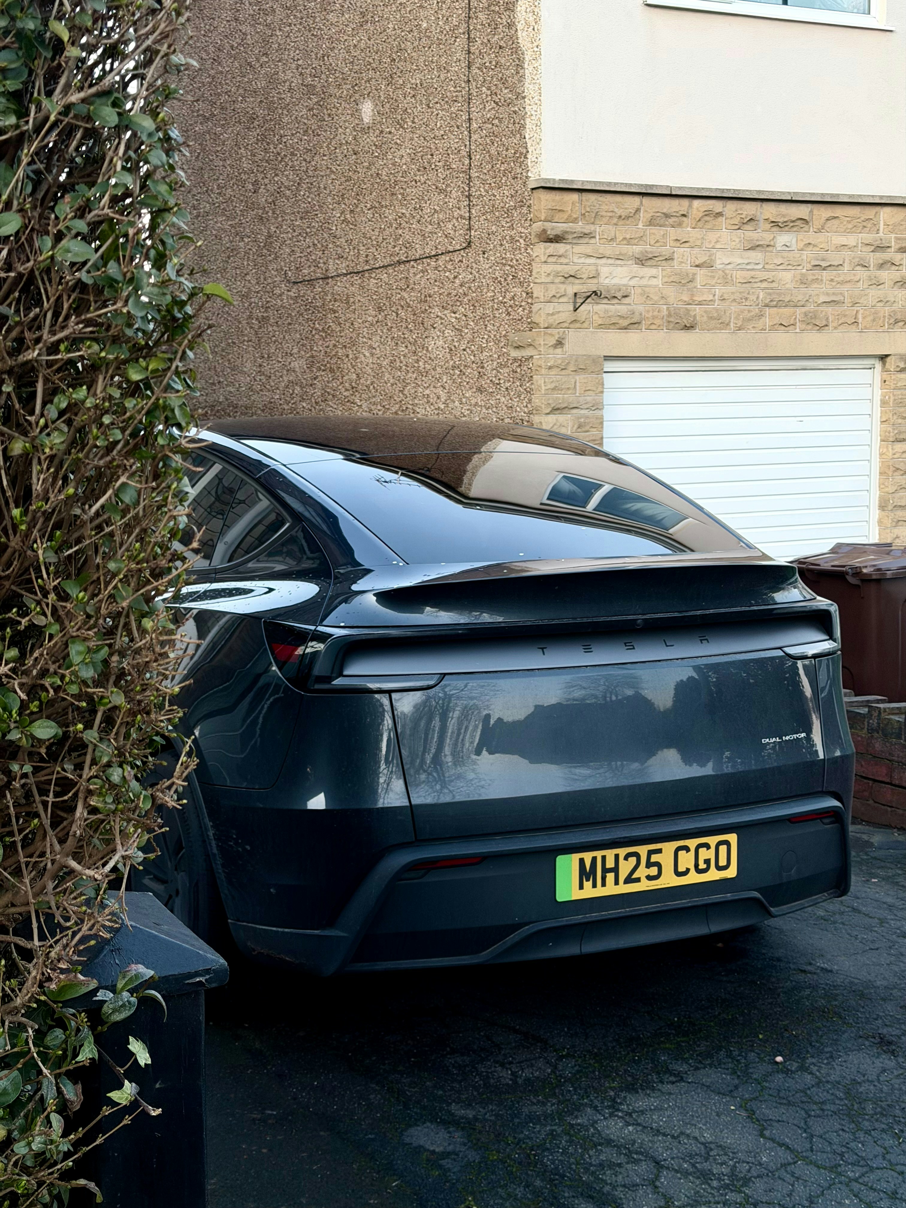 Dark-blue sedan tucked behind a hedge against a beige townhouse