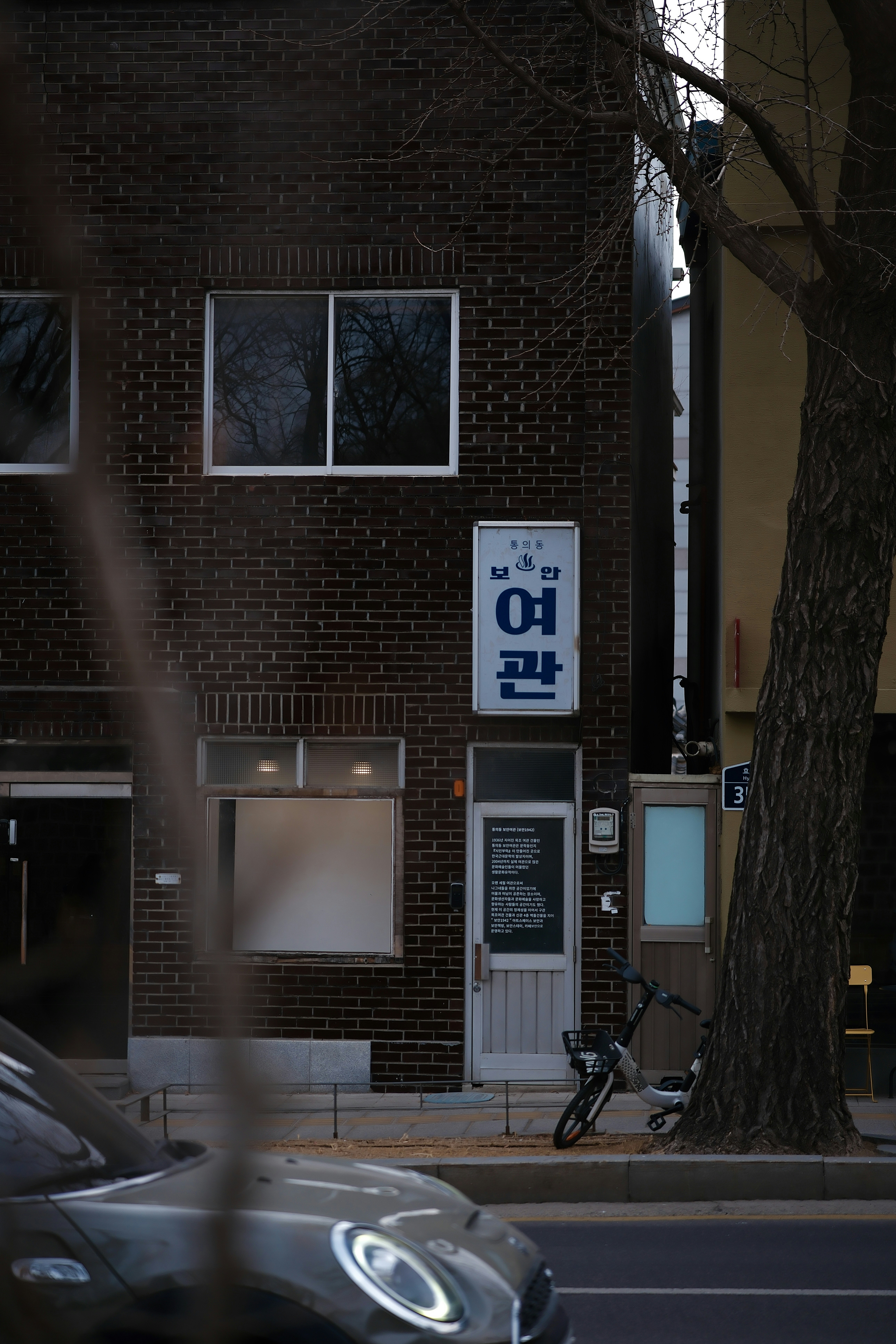 Blue Korean Sign Amid Brick Facade and Tree Trunk