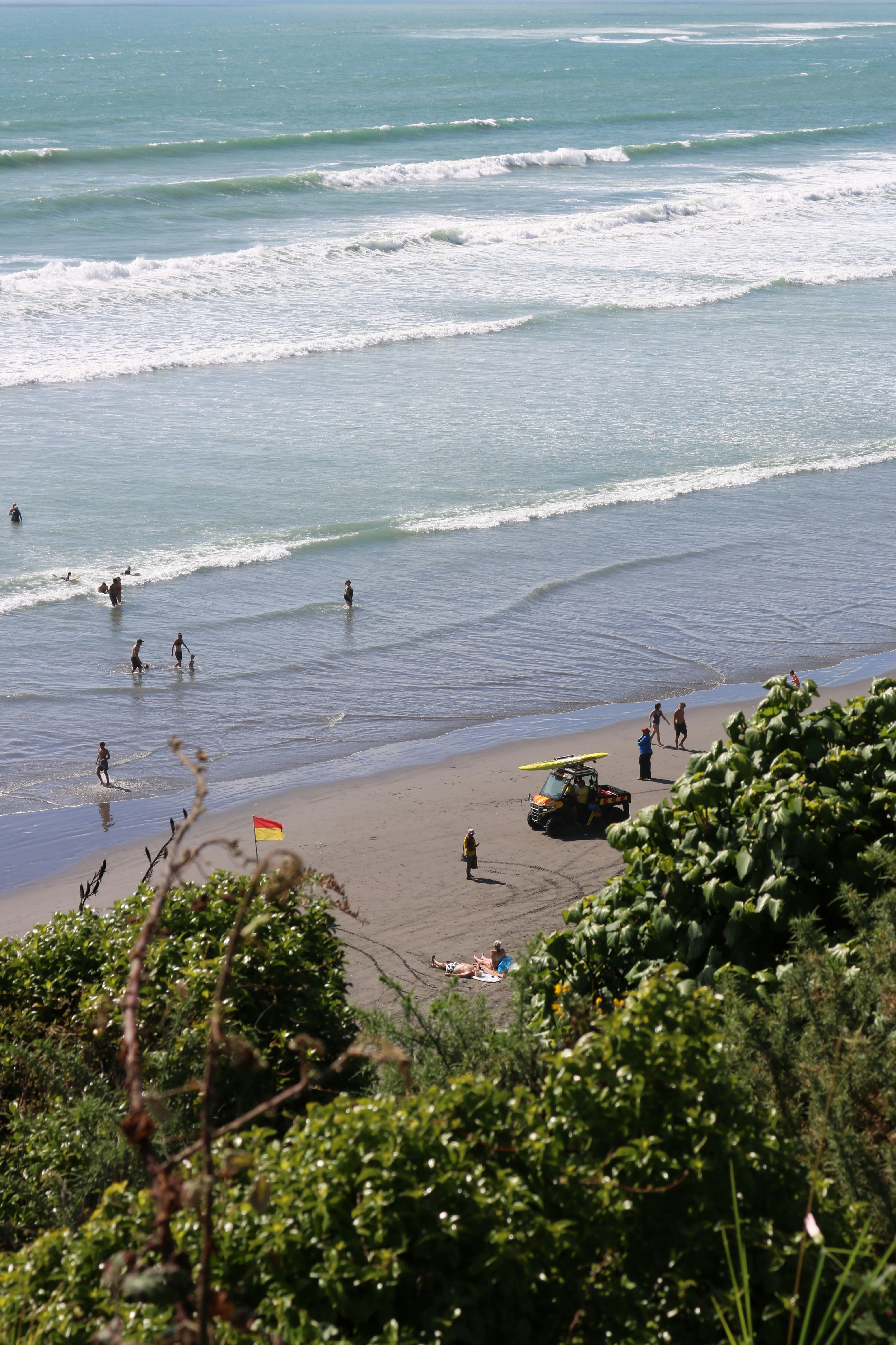 Sunlit Shoreline: A Kayak Cart and Beachgoers amid Turquoise Waves