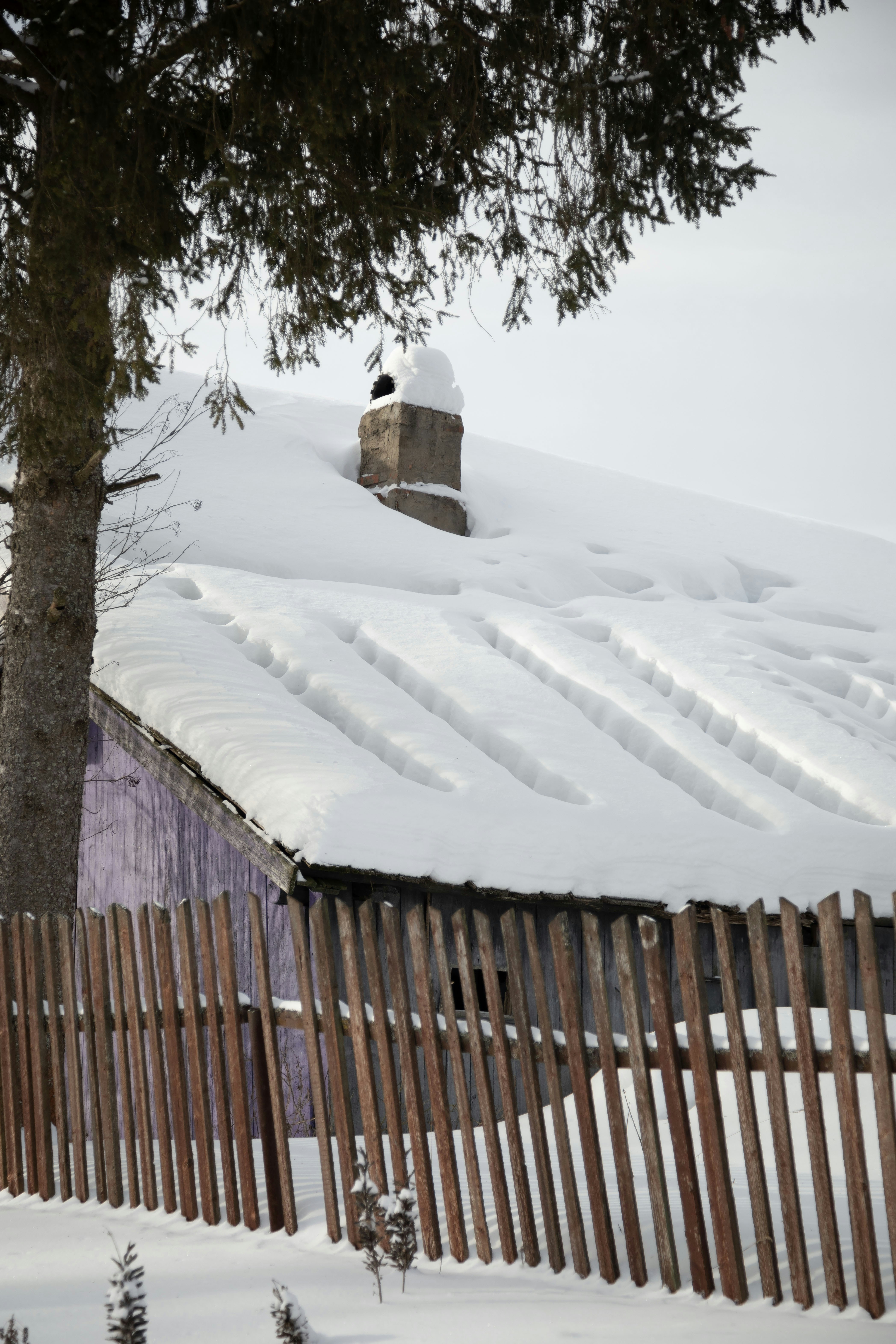 Snow-Covered Chimney on a Frosty Rooftop, Framed by a Wooden Fence