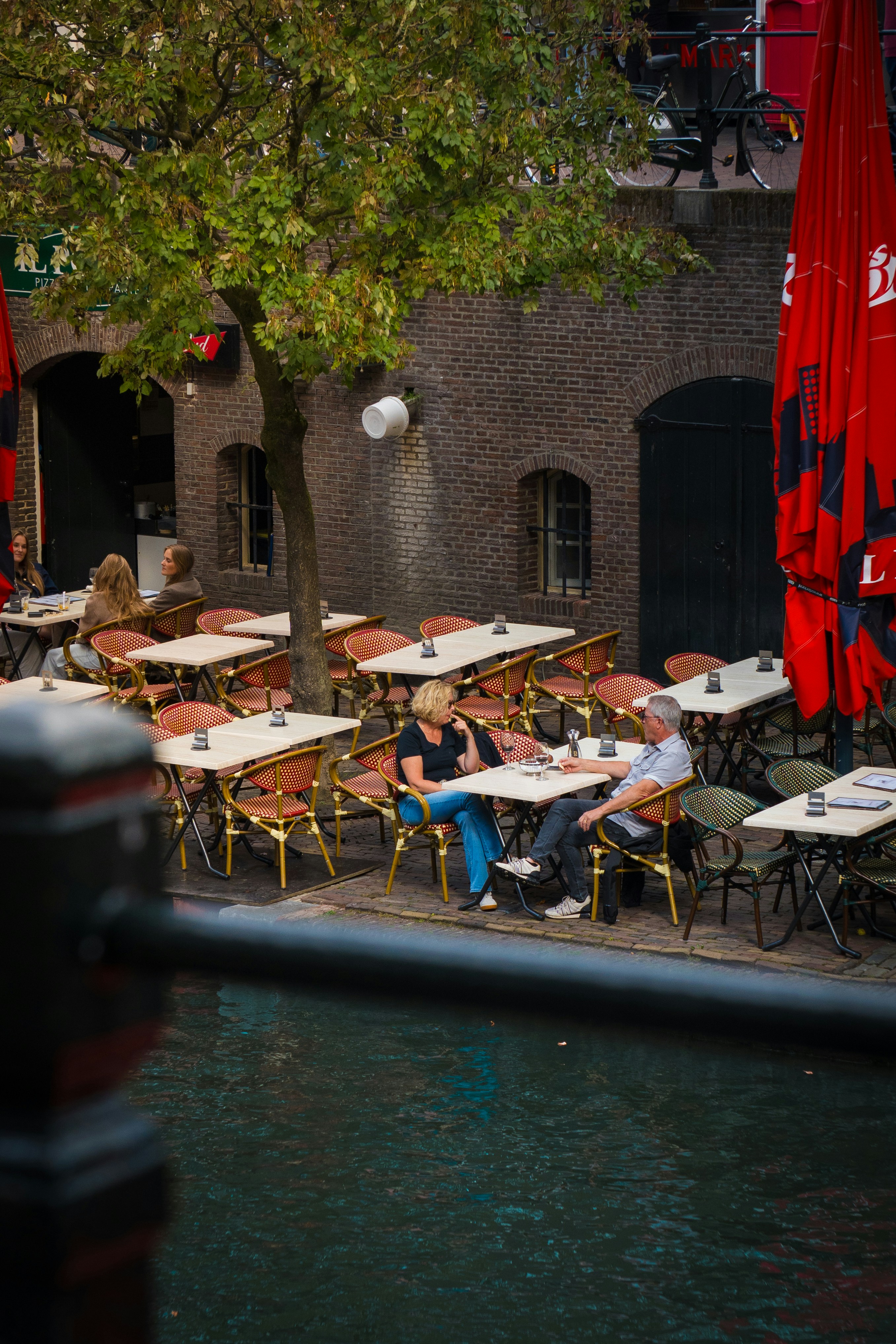 Canal-side Café Conversation Under Red Parasol Blades