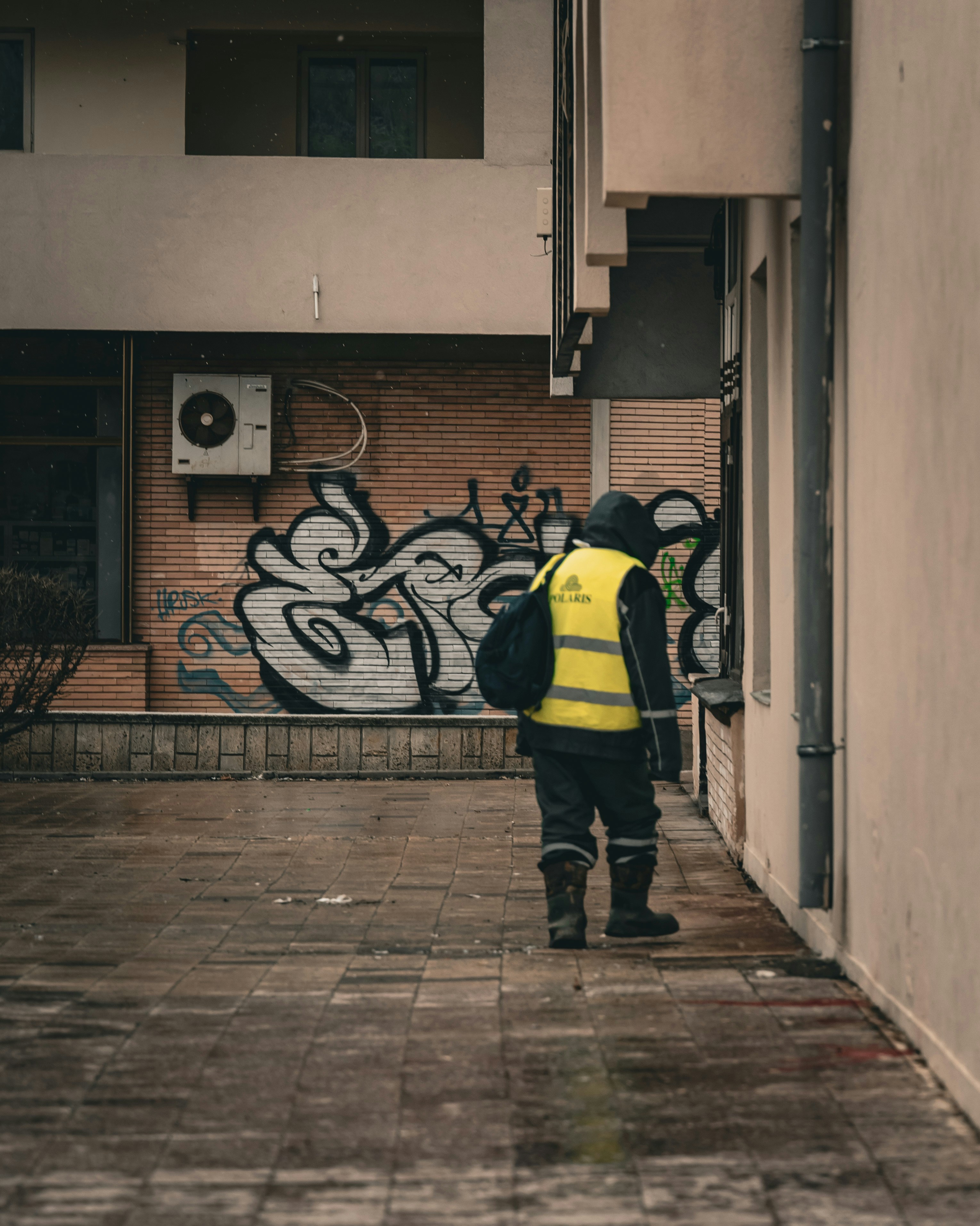 Forward Observer: A Worker in High-Visibility Glimpsed from a Graffiti-Walled Courtyard