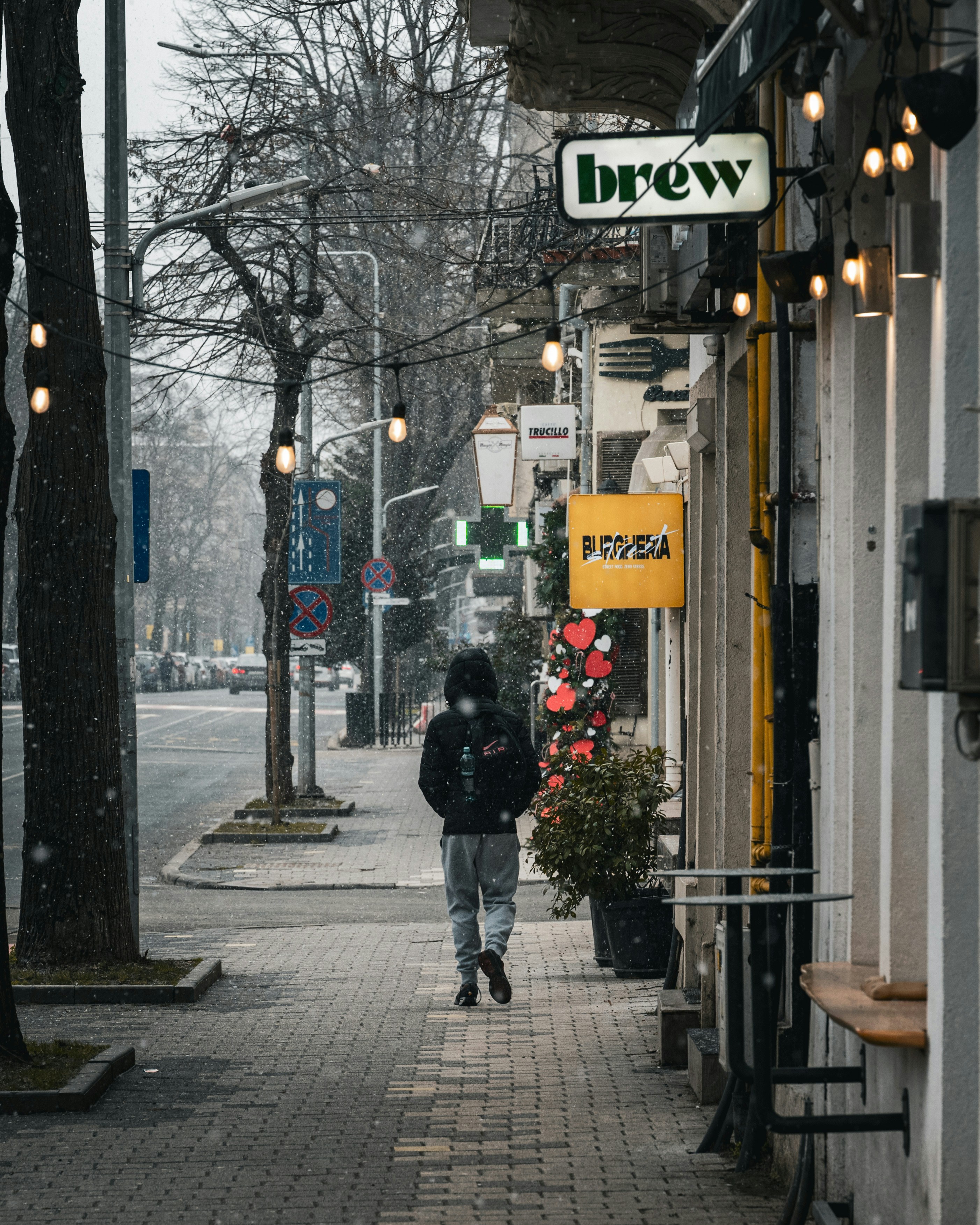 Snowy Street Crossing: A lone traveler walks toward the cafe glow