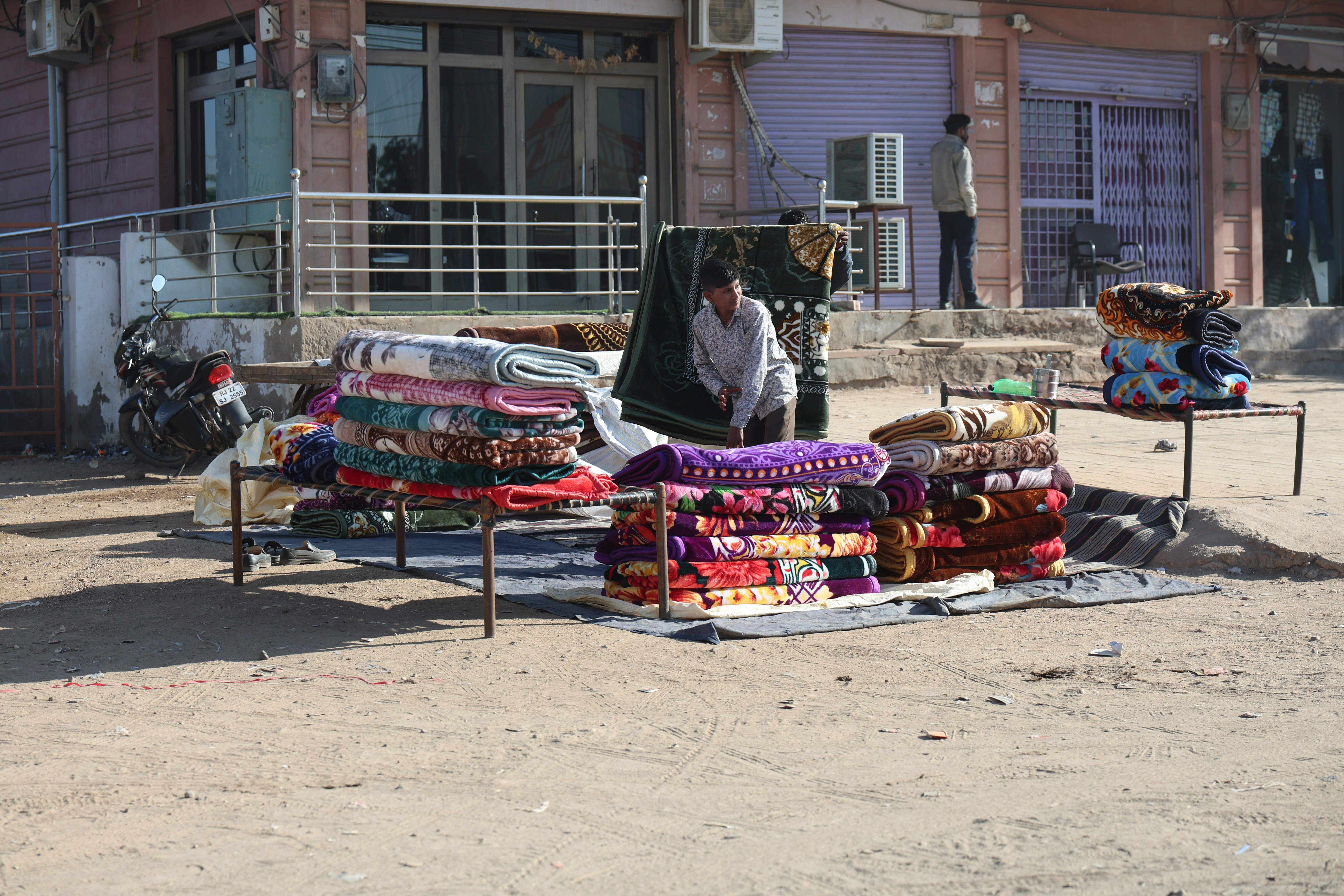 Streetside Textile Stand: A Vendor's Quiet Moment Amid Rugged Color