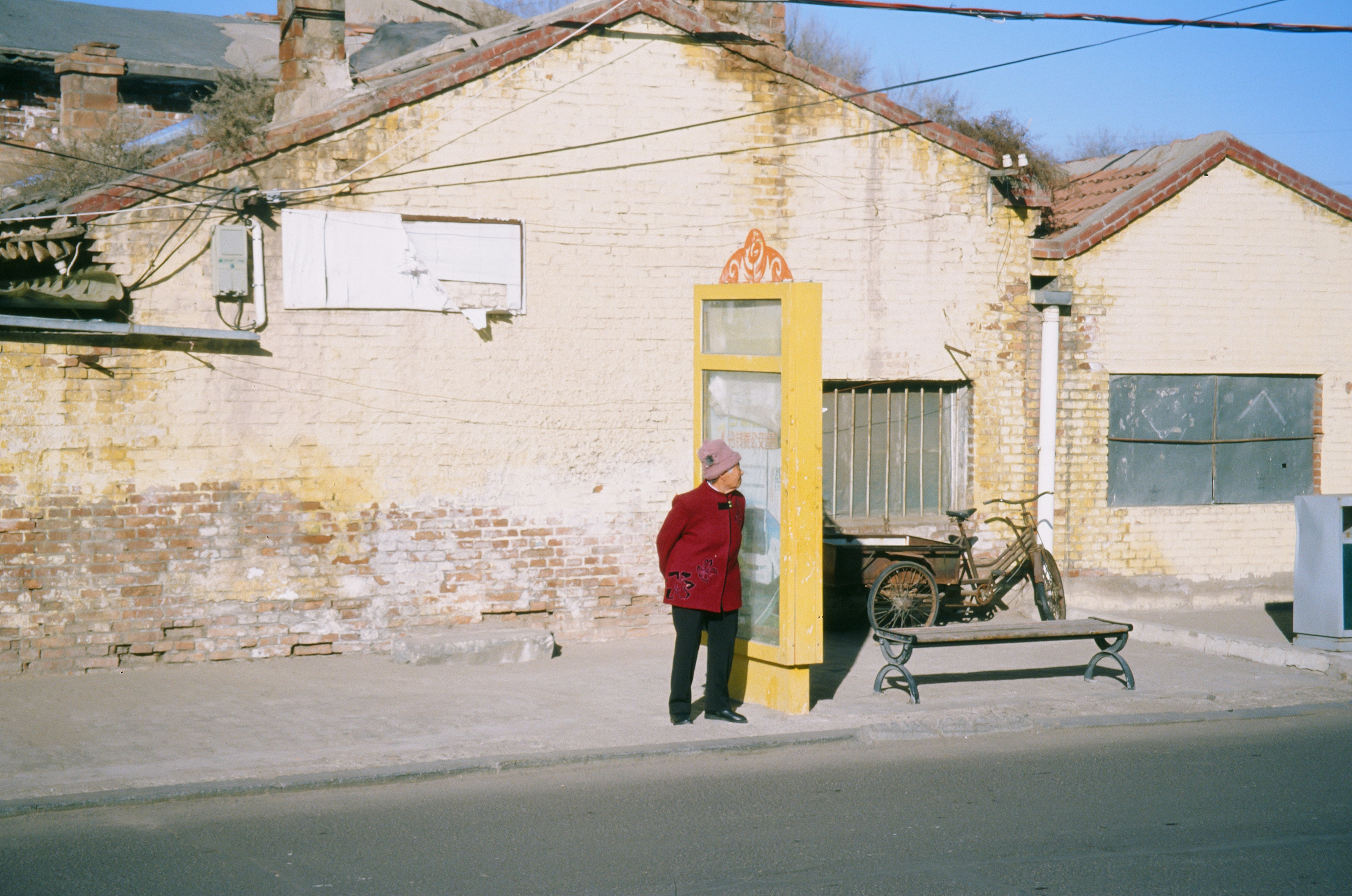 Elderly person standing by a yellow public phone booth.