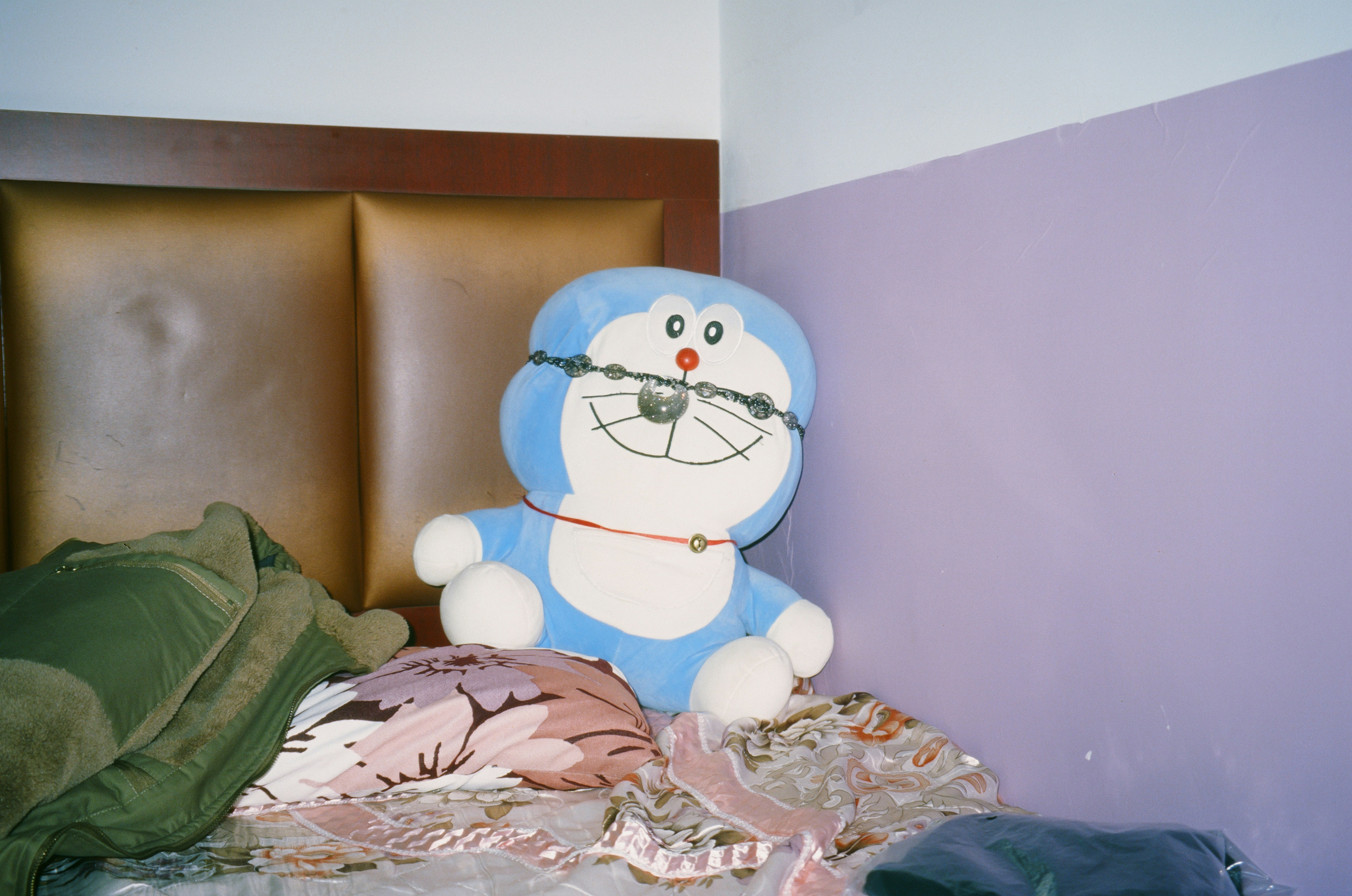 A blue doraemon plush toy sits on a bed.