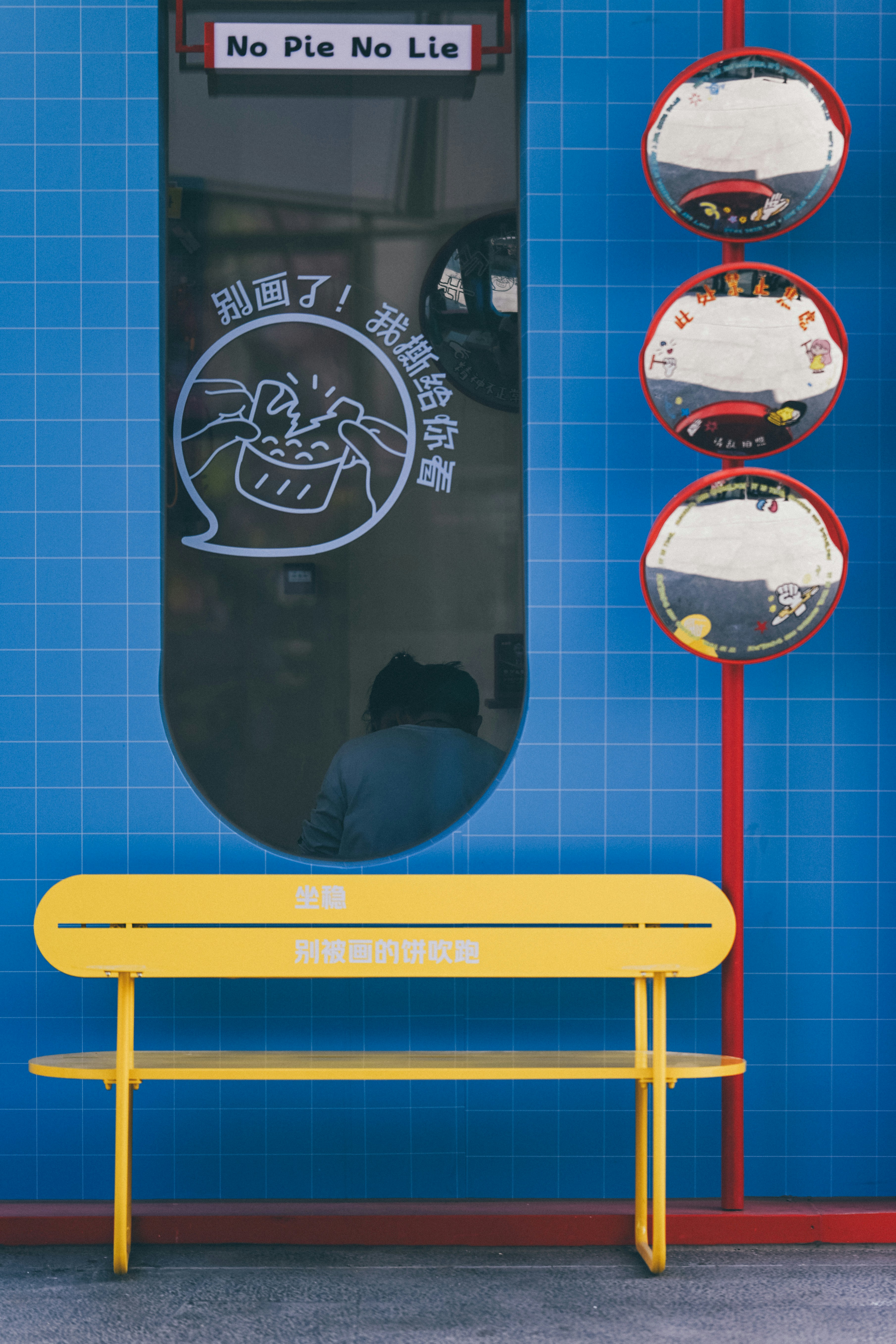 Blue facade, yellow bench, and circular mirrors: a playful street scene