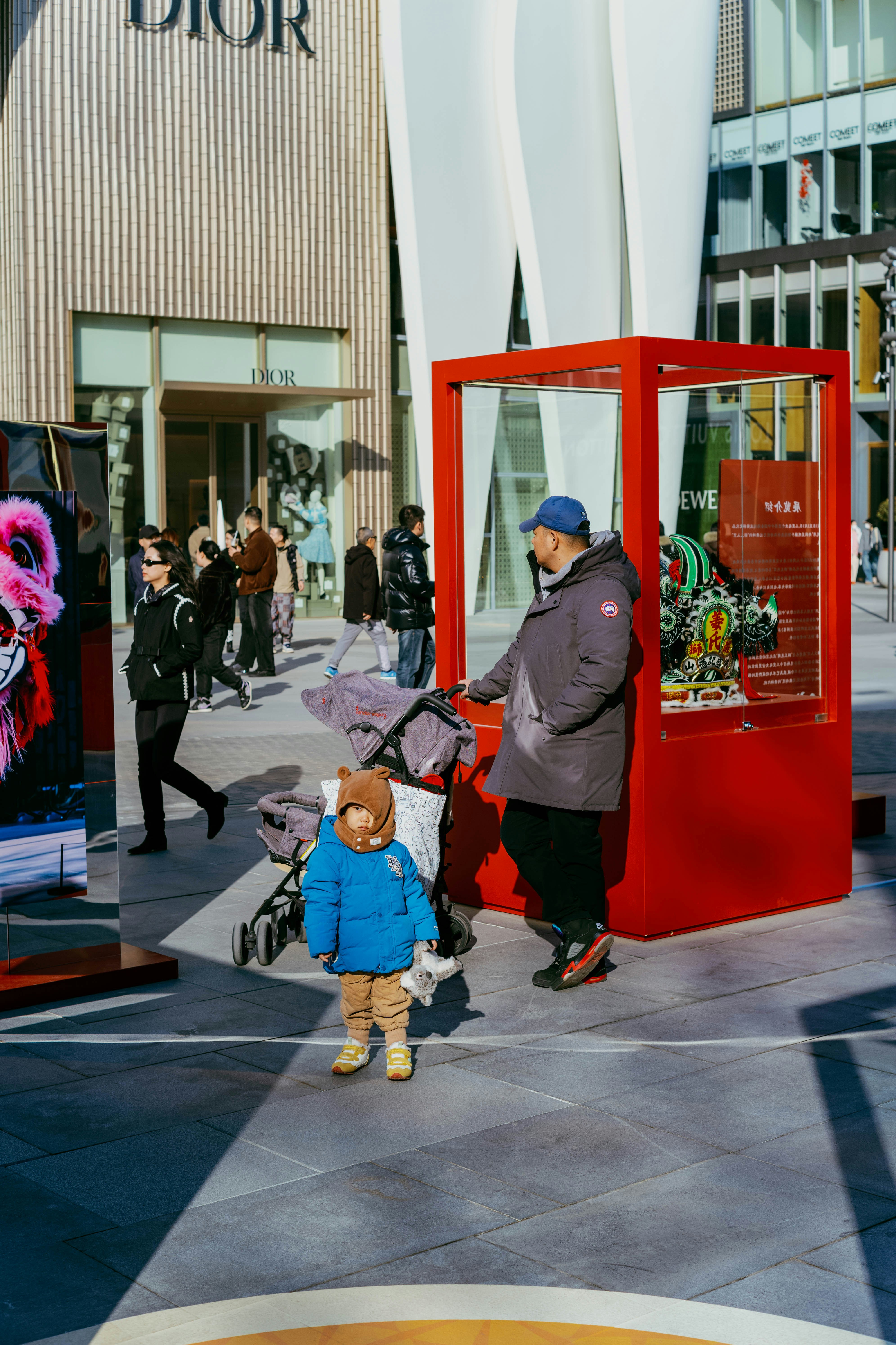 Child in blue coat and father near red exhibit stand in a busy city plaza