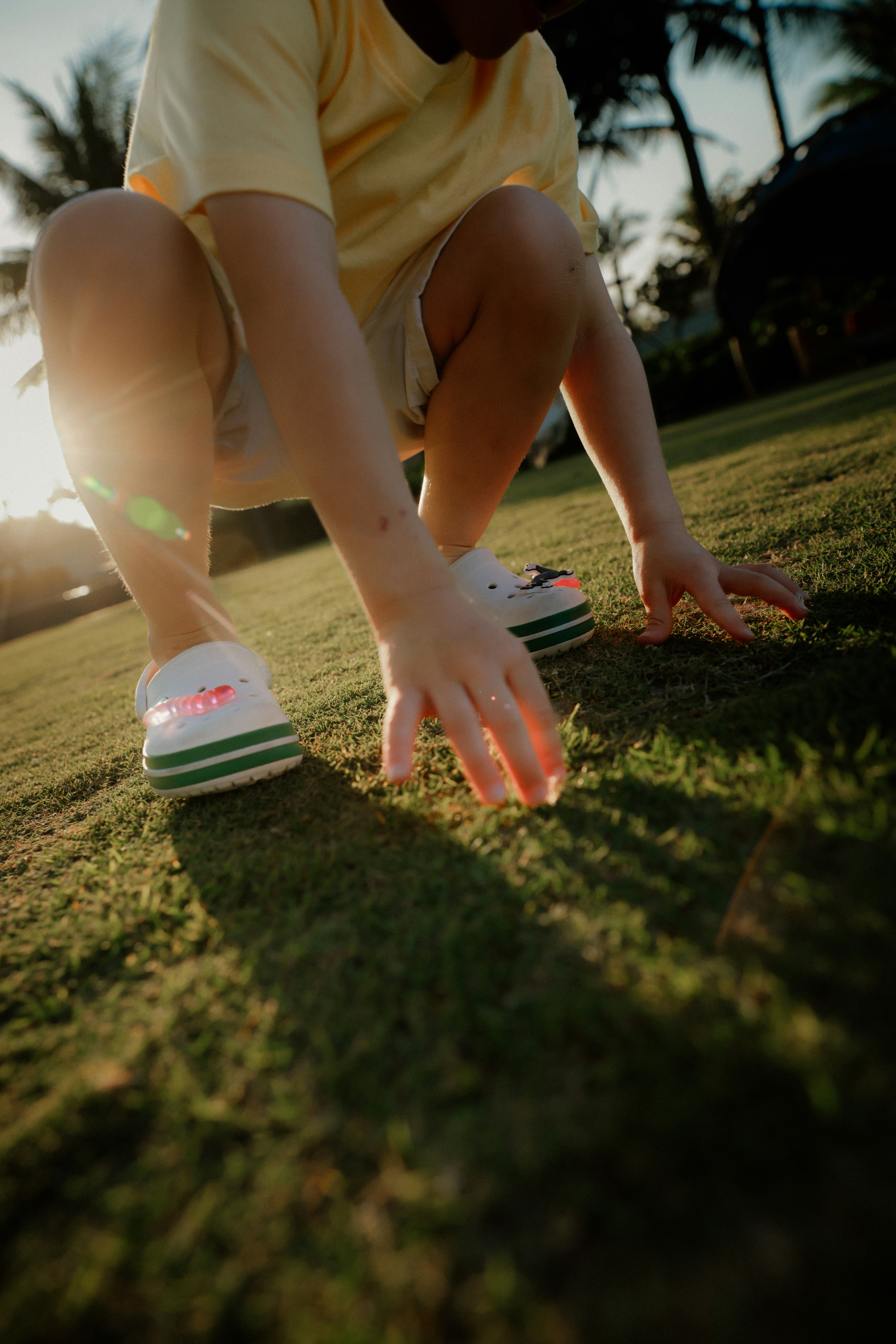 Grounded Reach: A Child’s Hands and Sneakers on Sunlit Grass