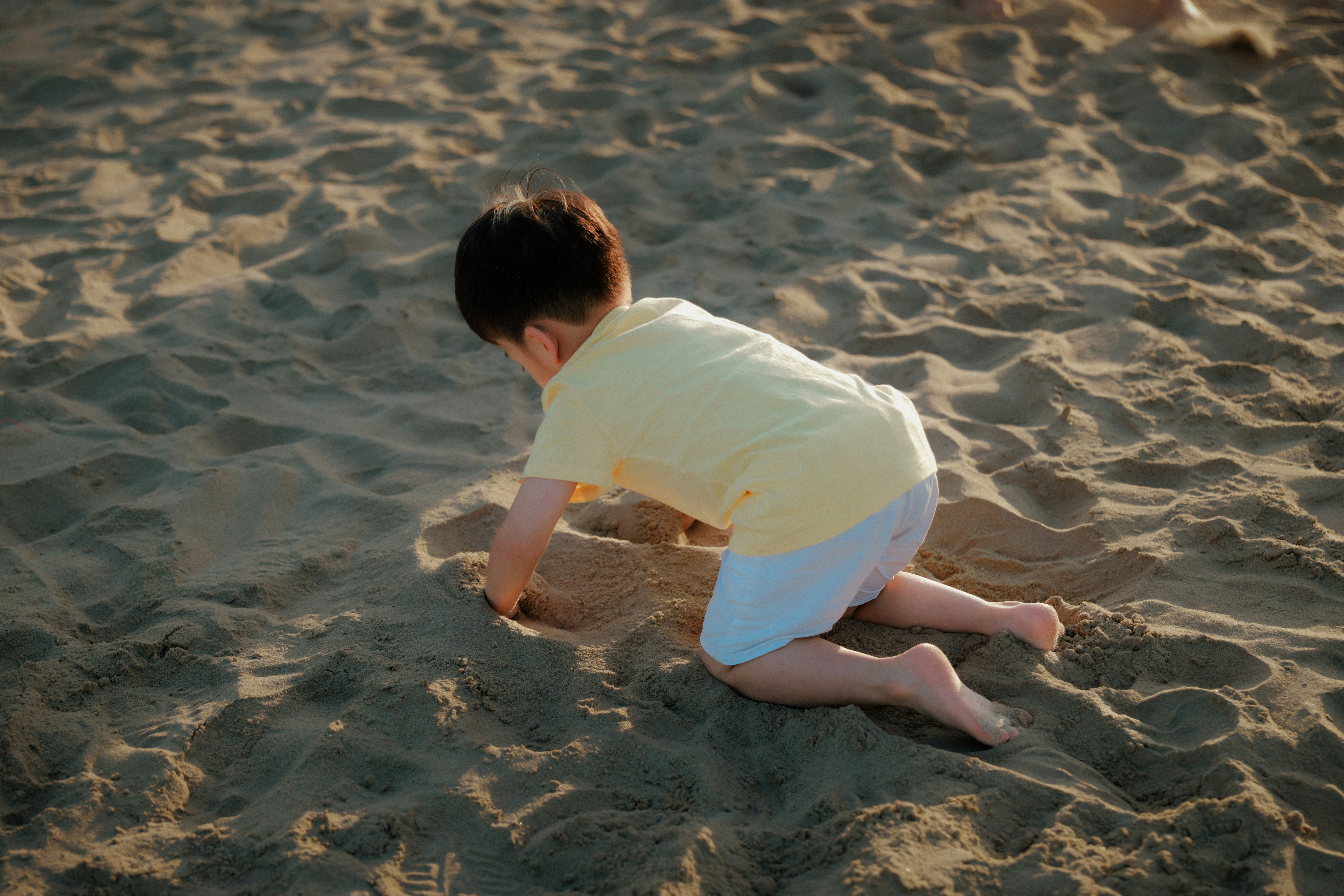 Child in soft golden hour light digging in a sandy playground