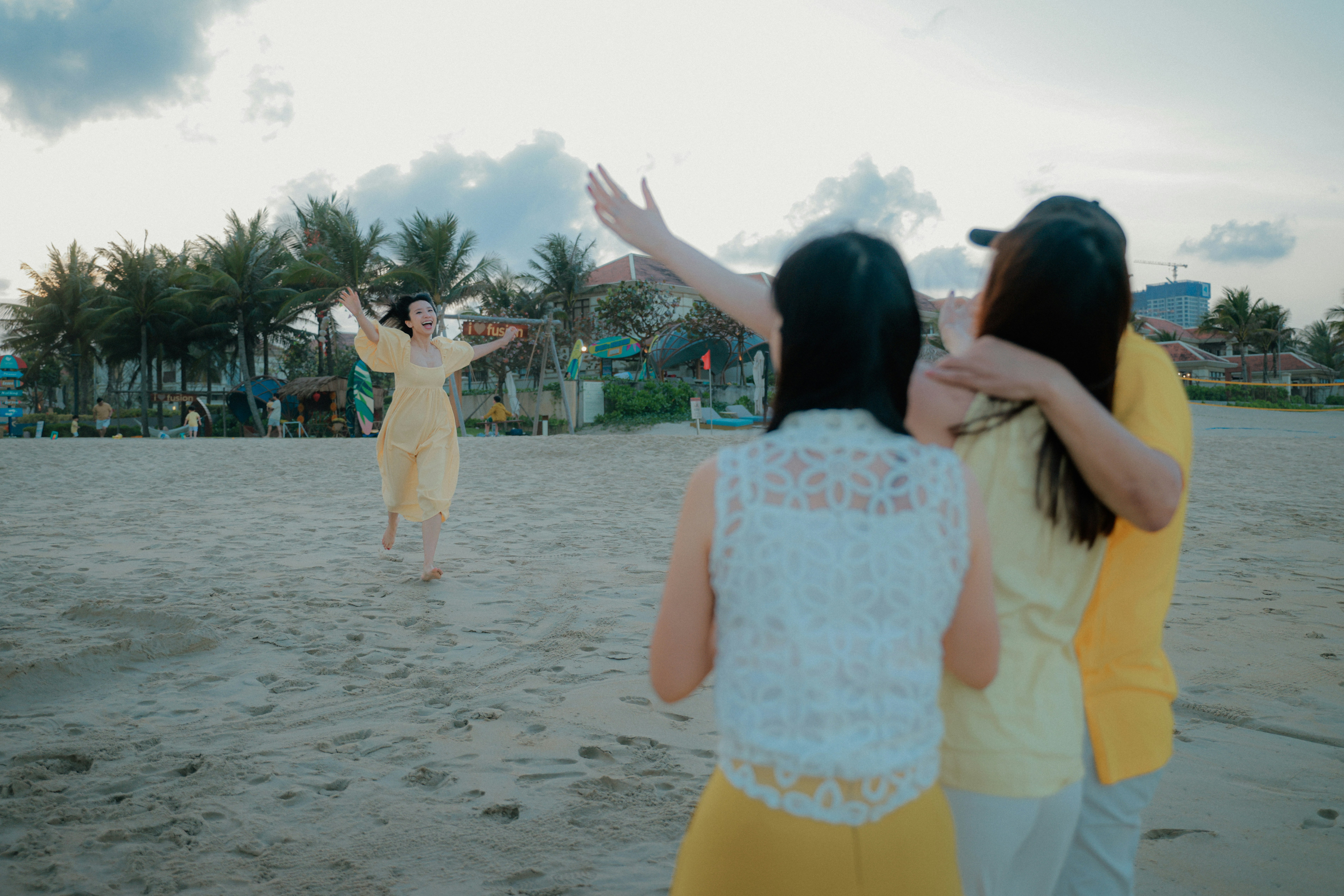 Three friends on a sunlit beach celebrate with open arms as one runs toward them