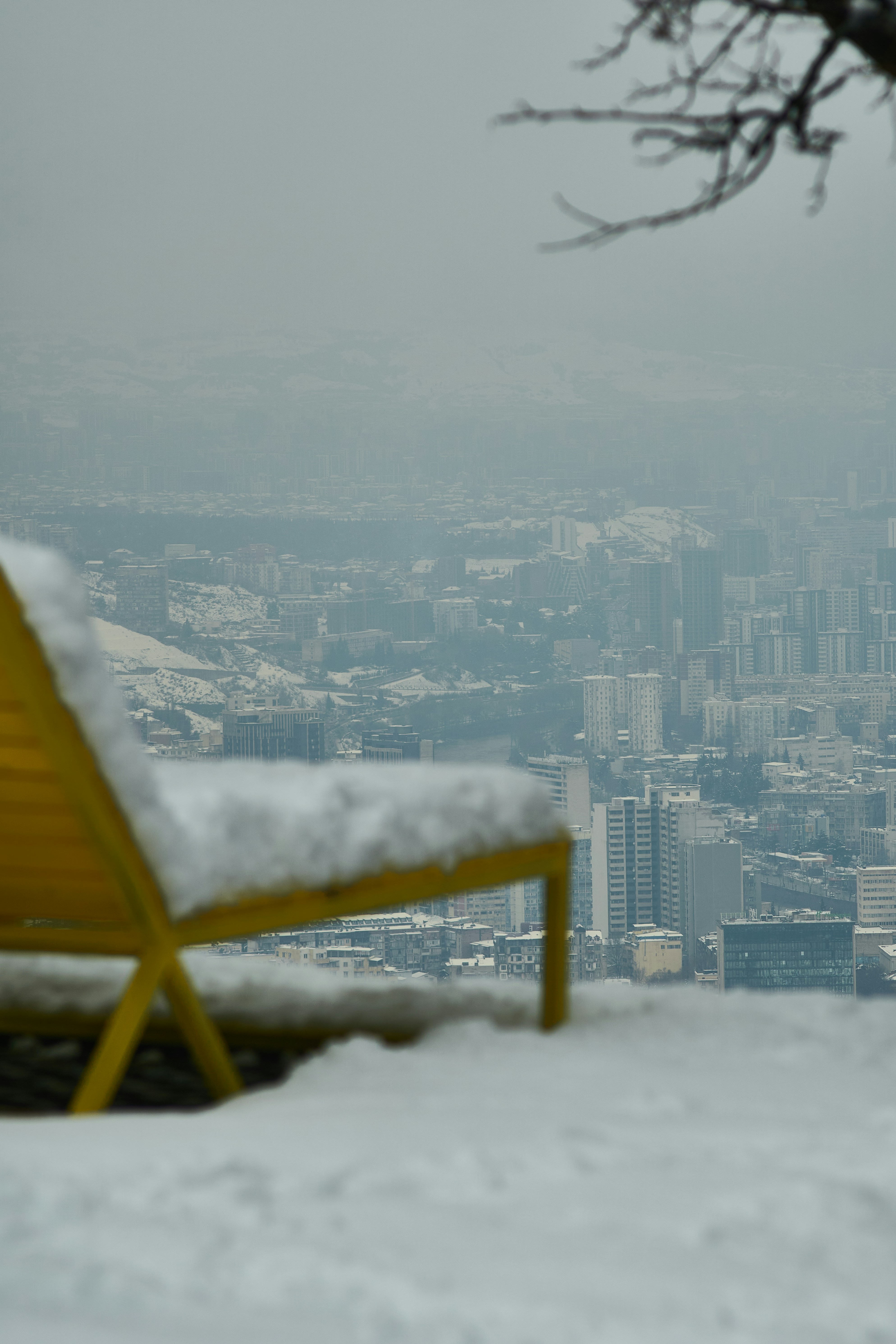 Snowy Terrace with Distant Cityscape and Yellow Lounge Chair