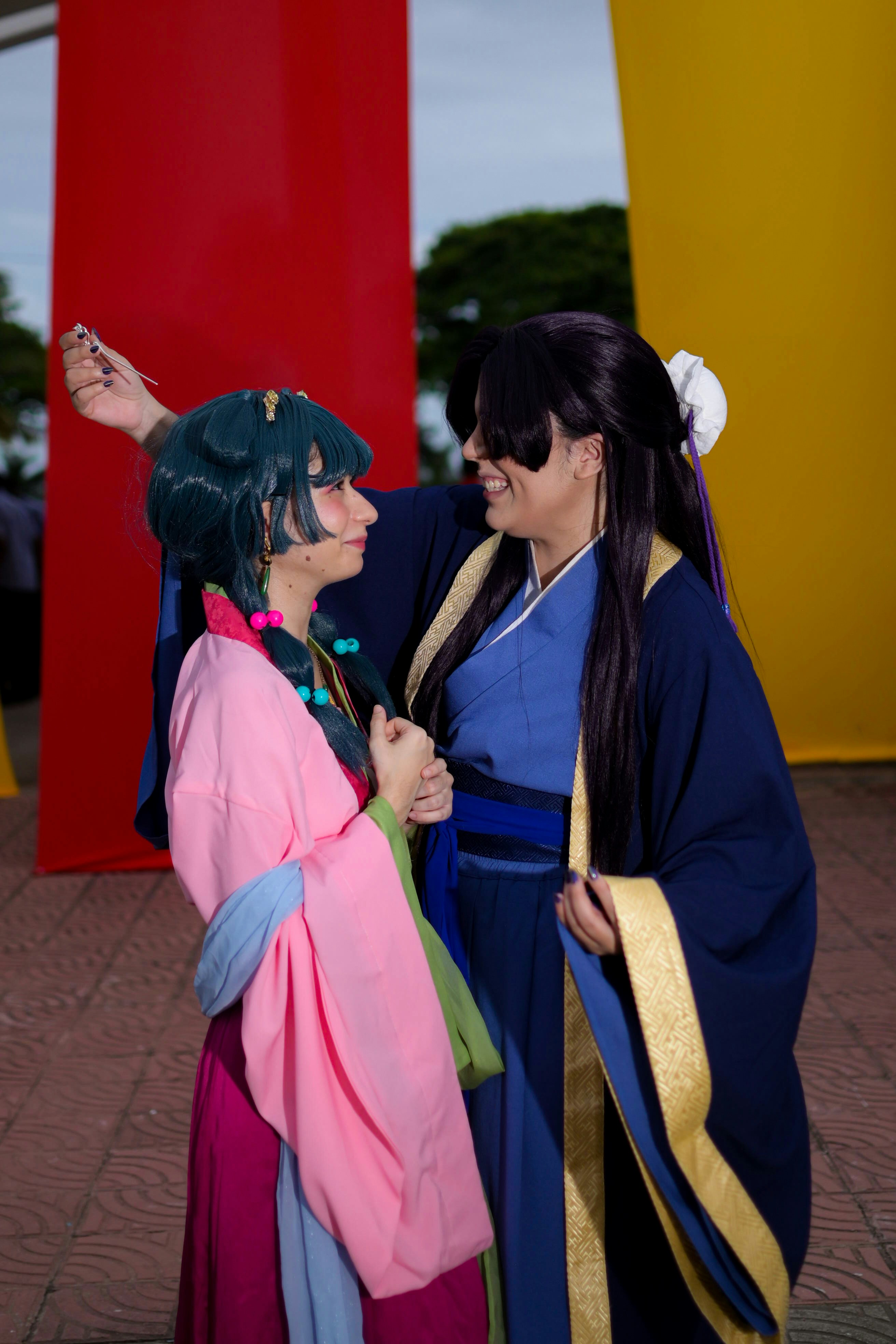 Two cosplayers share a playful moment under bold festival banners