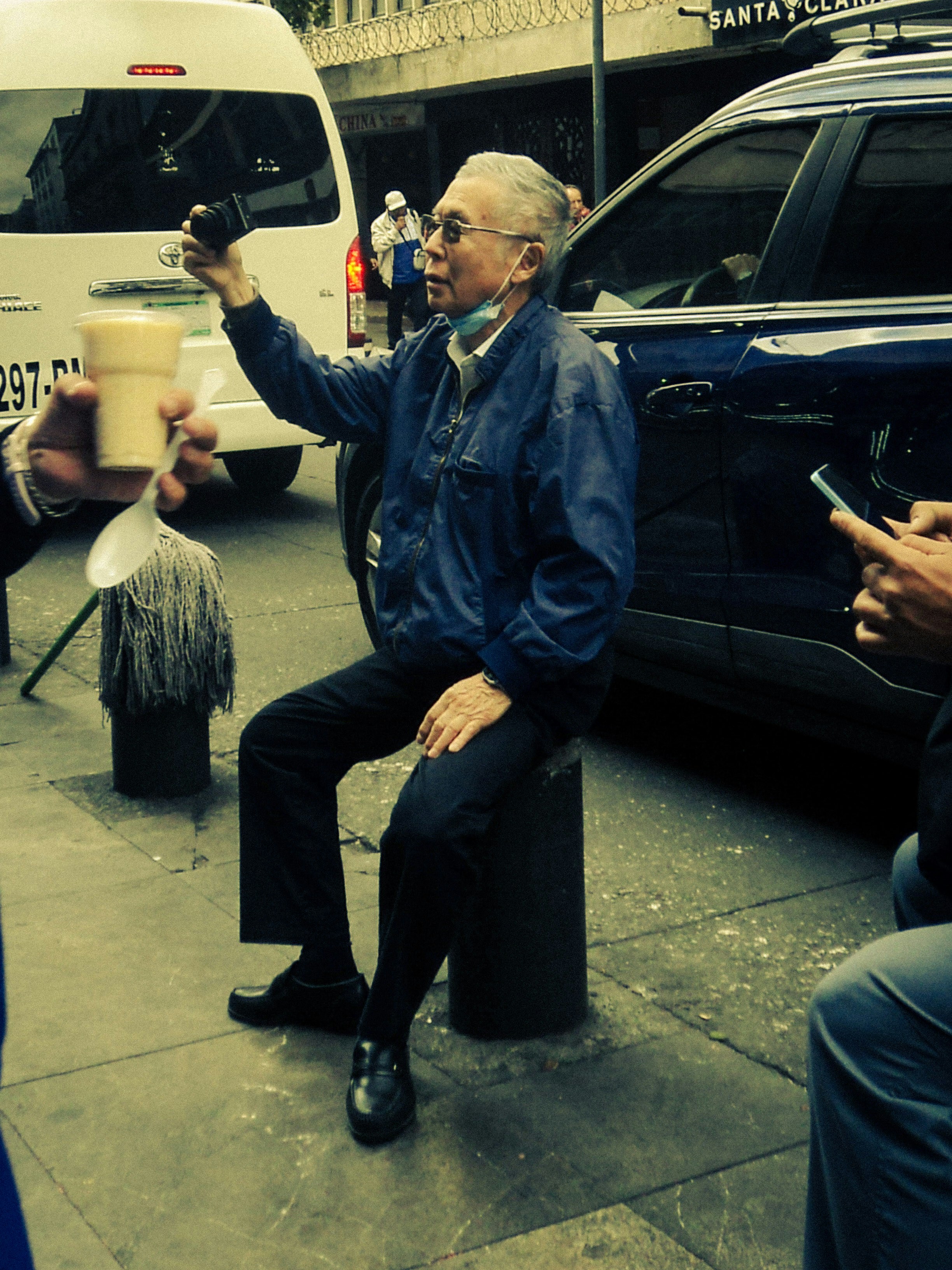 Elderly man takes a selfie with a camera on street.