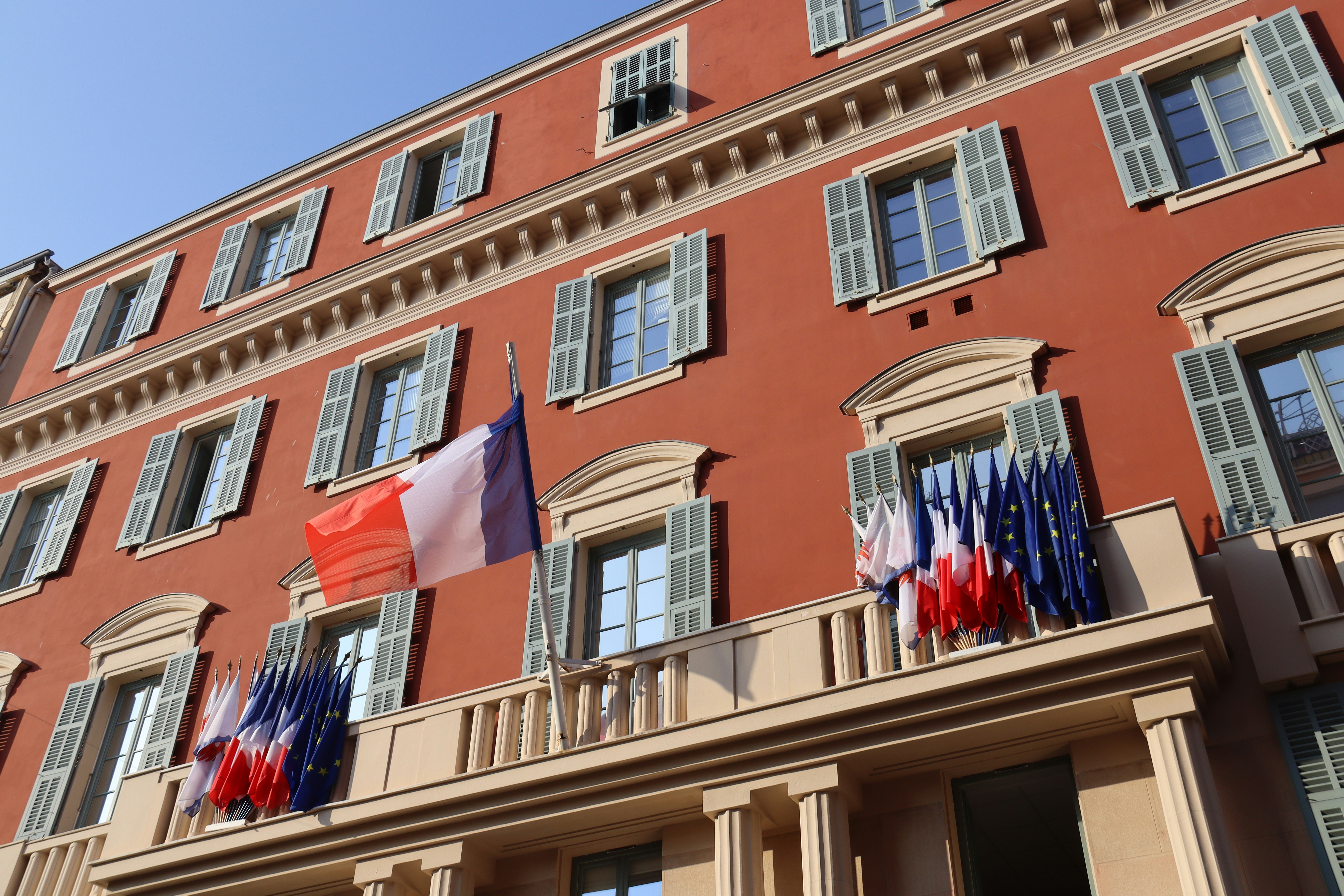 Flags and façade: French tricolor flutter above a sunlit grand doorway