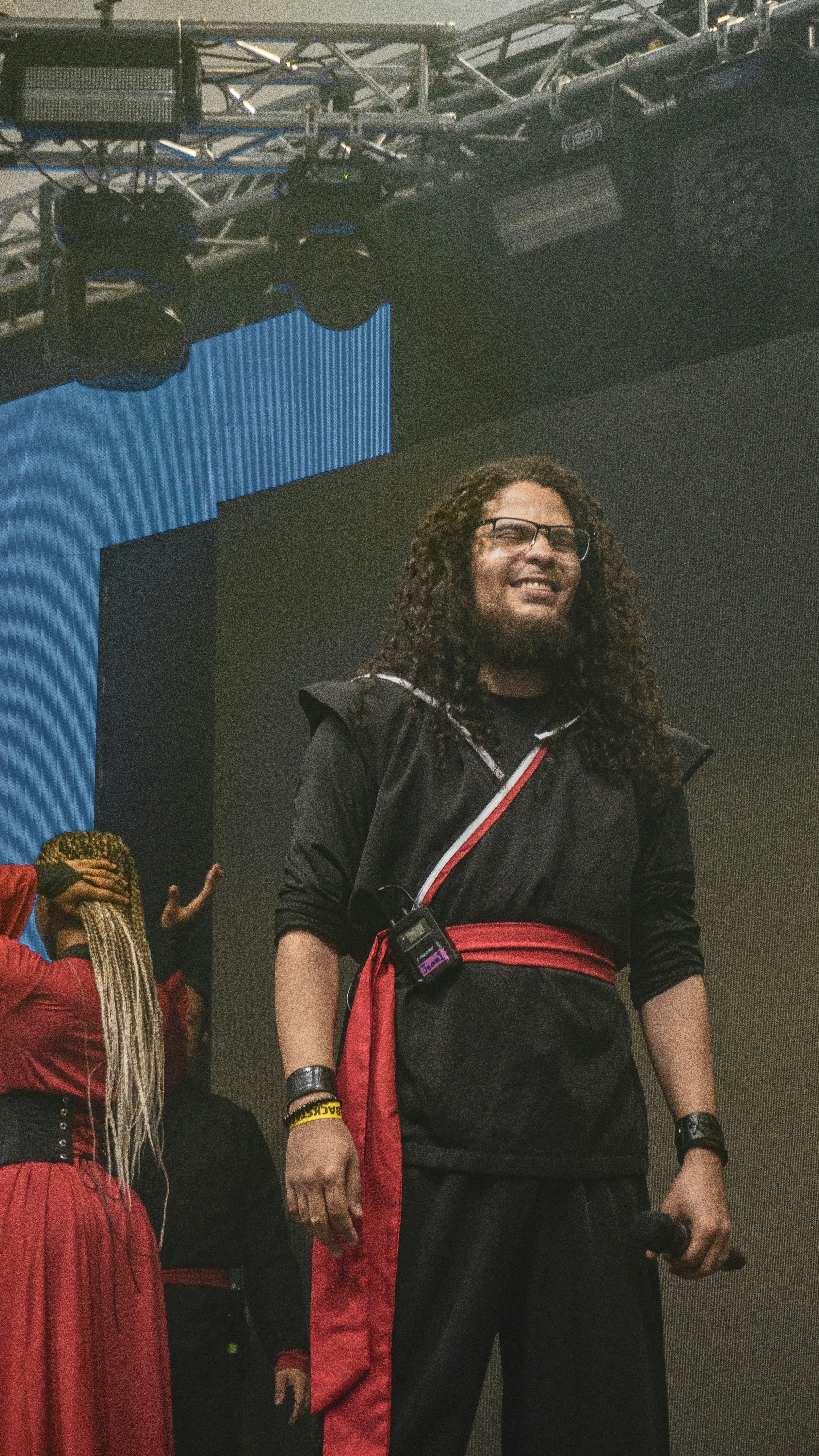 Stage Presence: A Performer in Bold Black with Red Sash Under Stage Lights