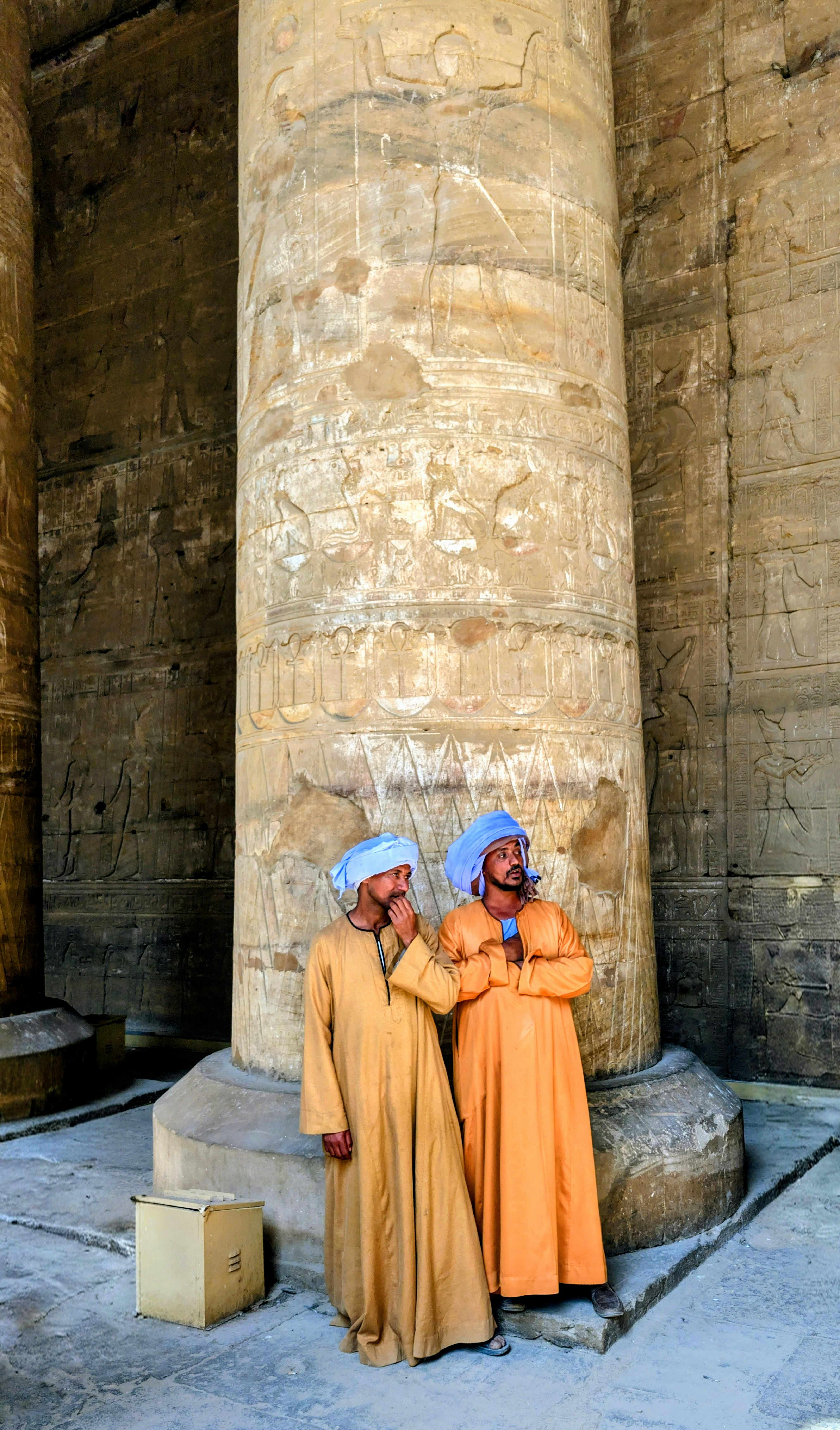 Two men in traditional clothing stand by a large column.