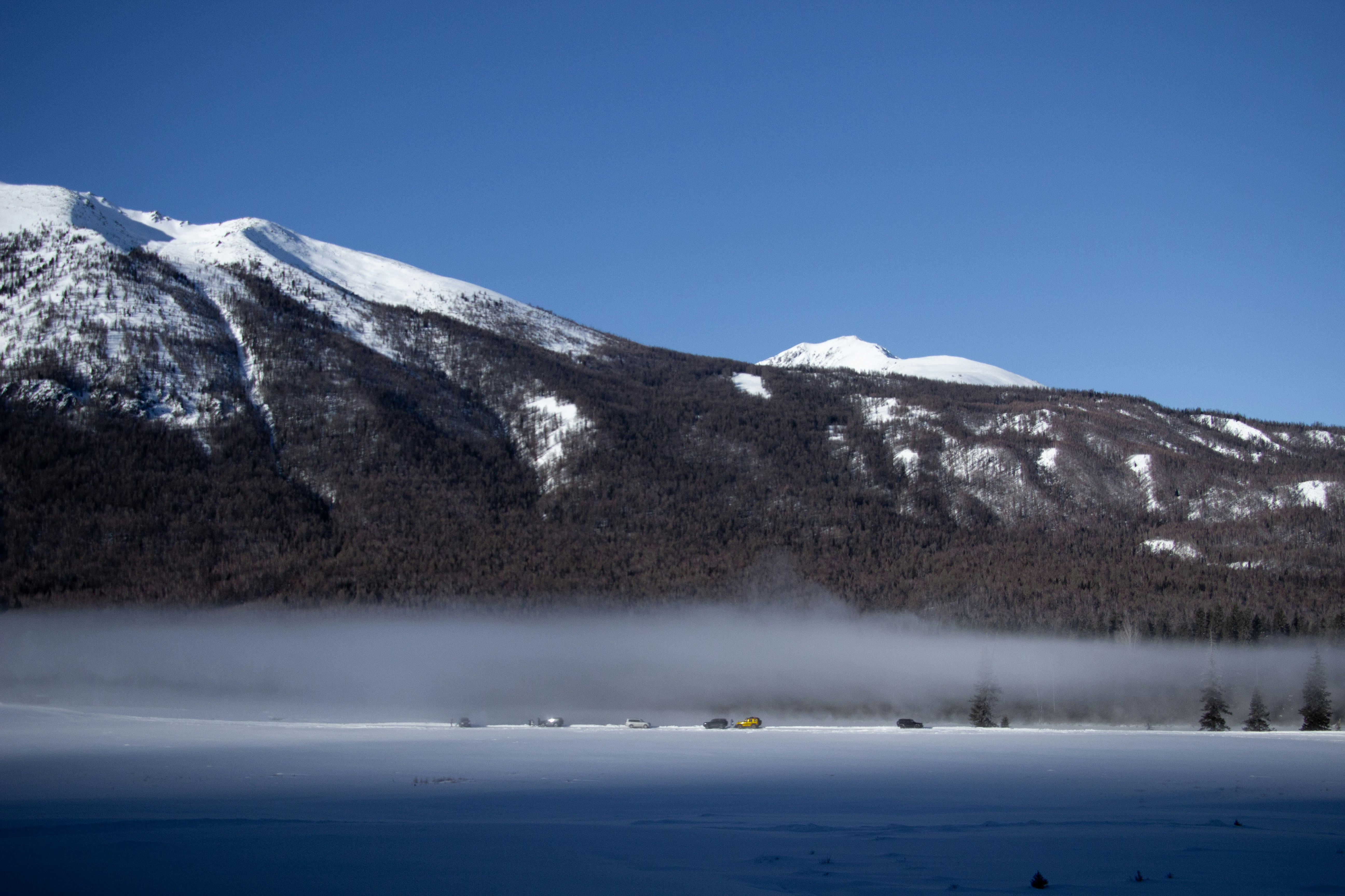 Snow-dusted ridgeline under a crisp cobalt sky with fog-rimmed lake