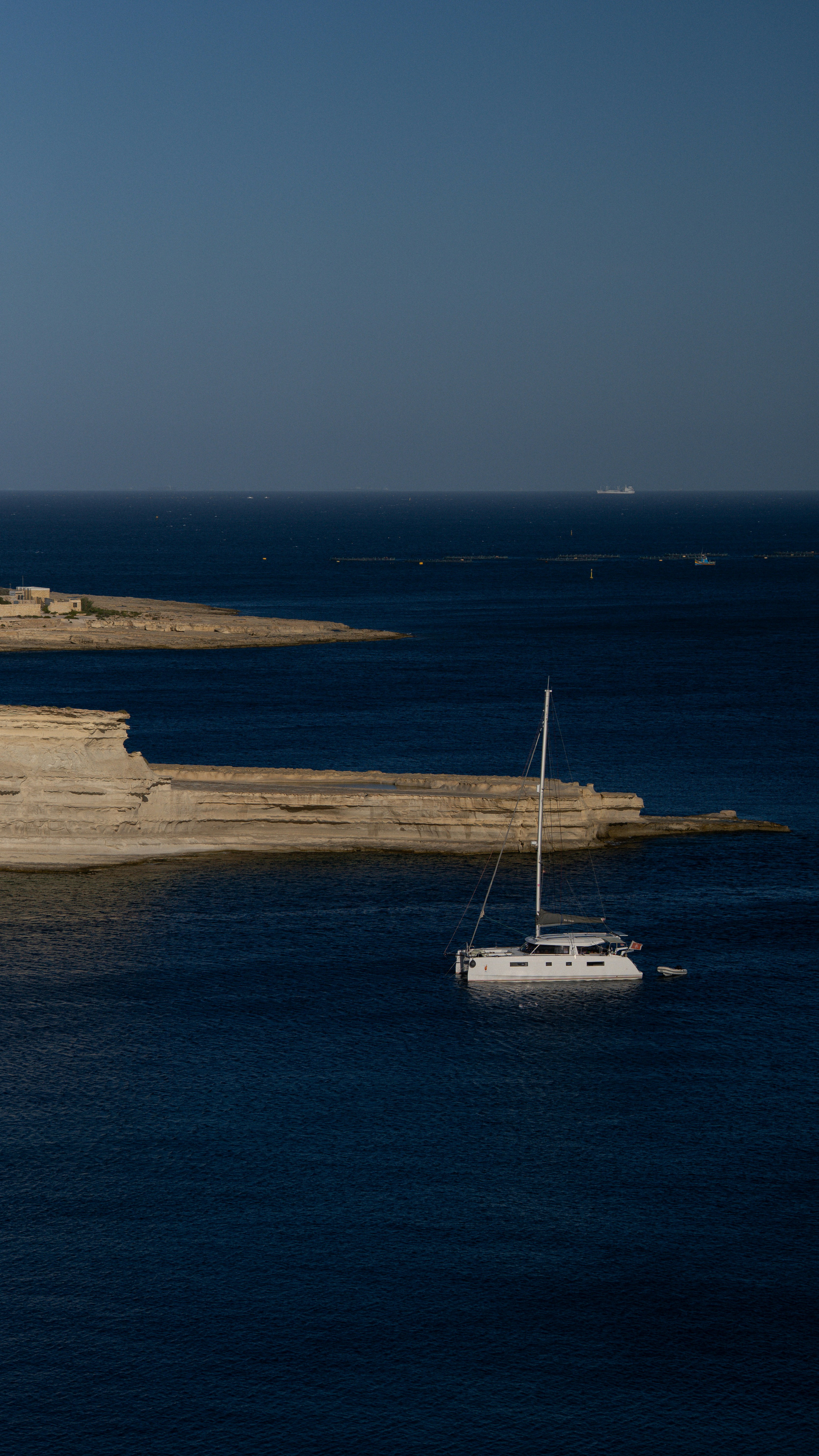 Sailboat Nestled Against Limestone shores under a Vast Cerulean Sky